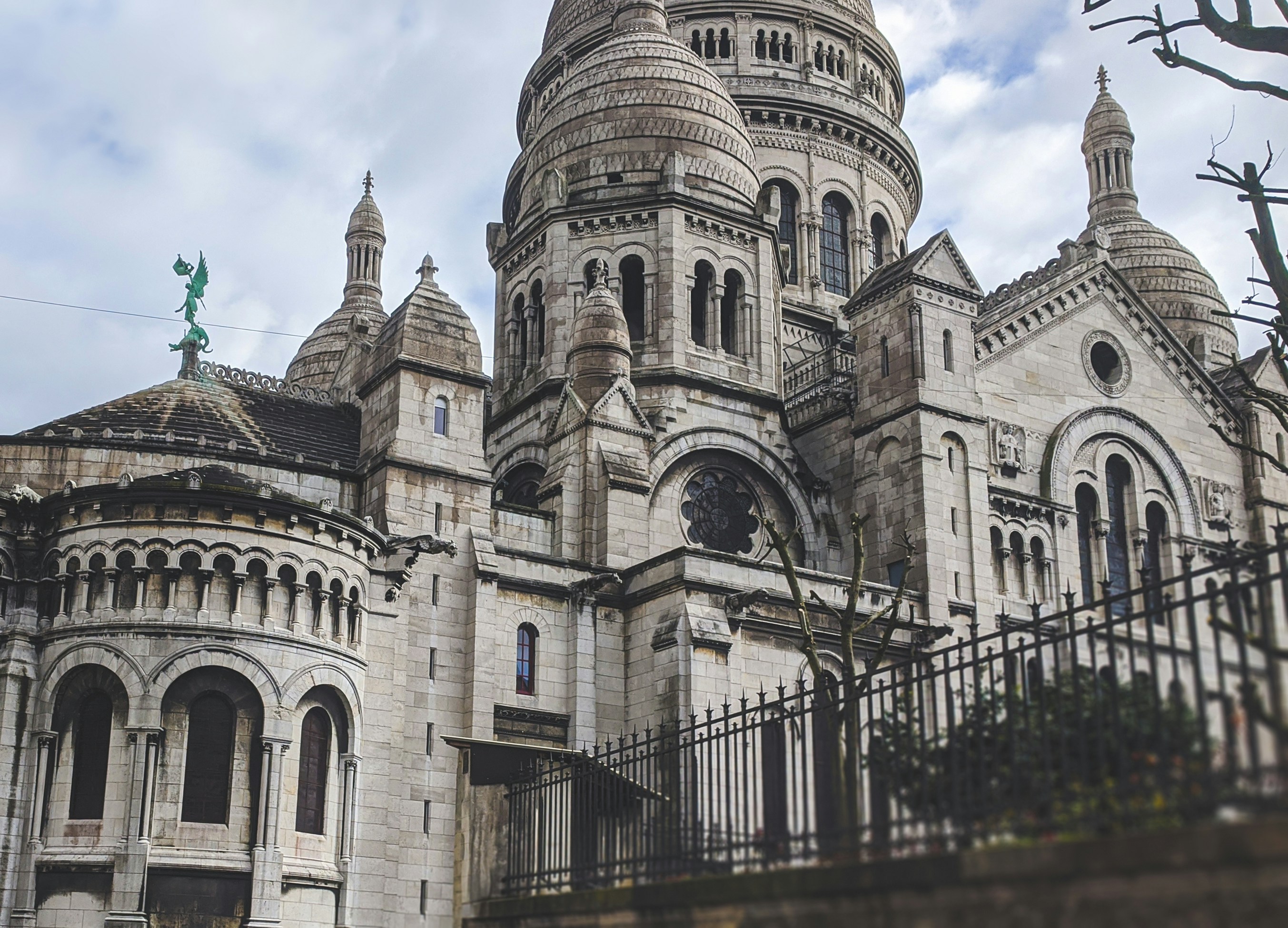 Stone basilica with domed towers under a cloudy sky.