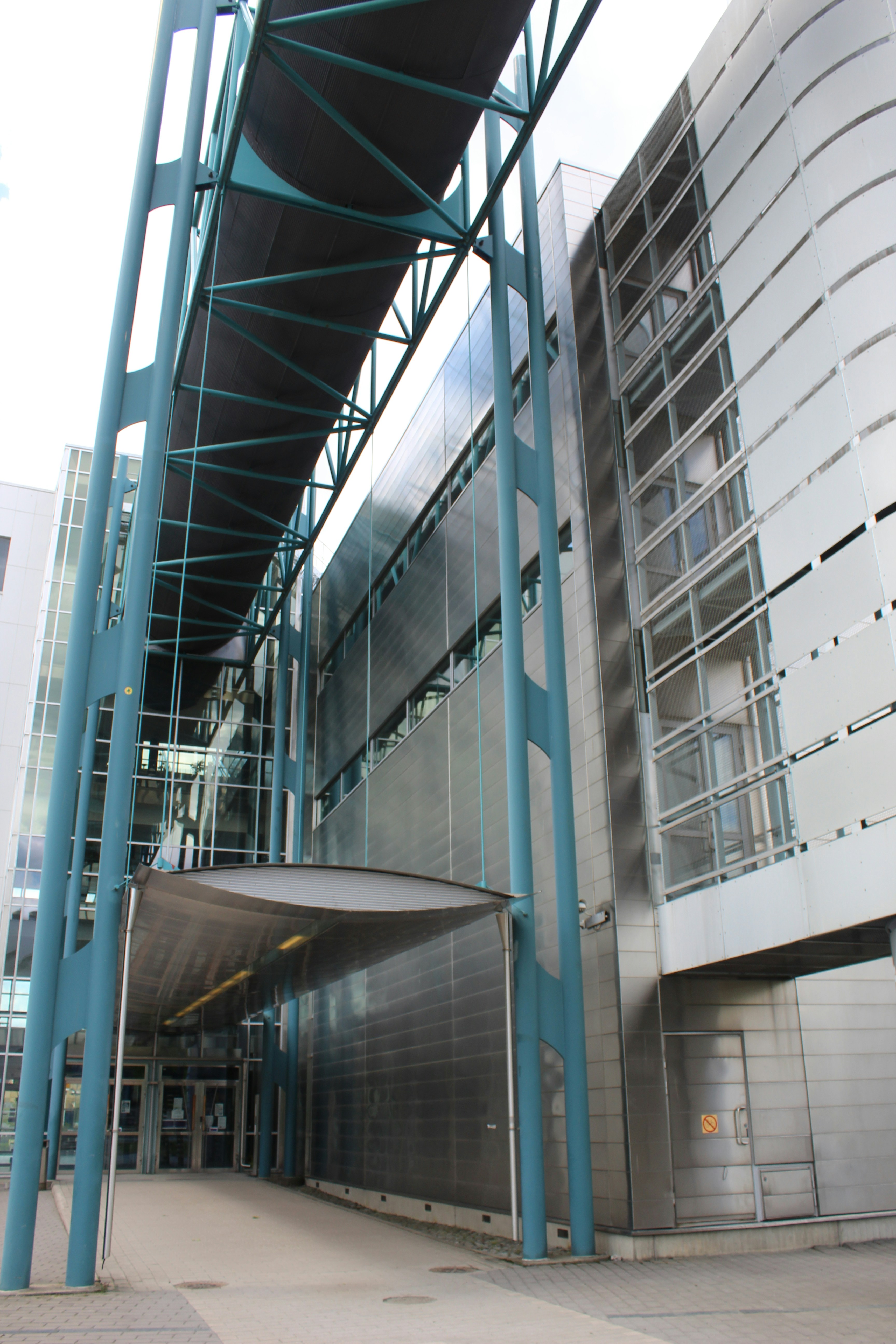 Sleek, metallic building entrance with a suspended walkway, showcasing contemporary architectural design elements.