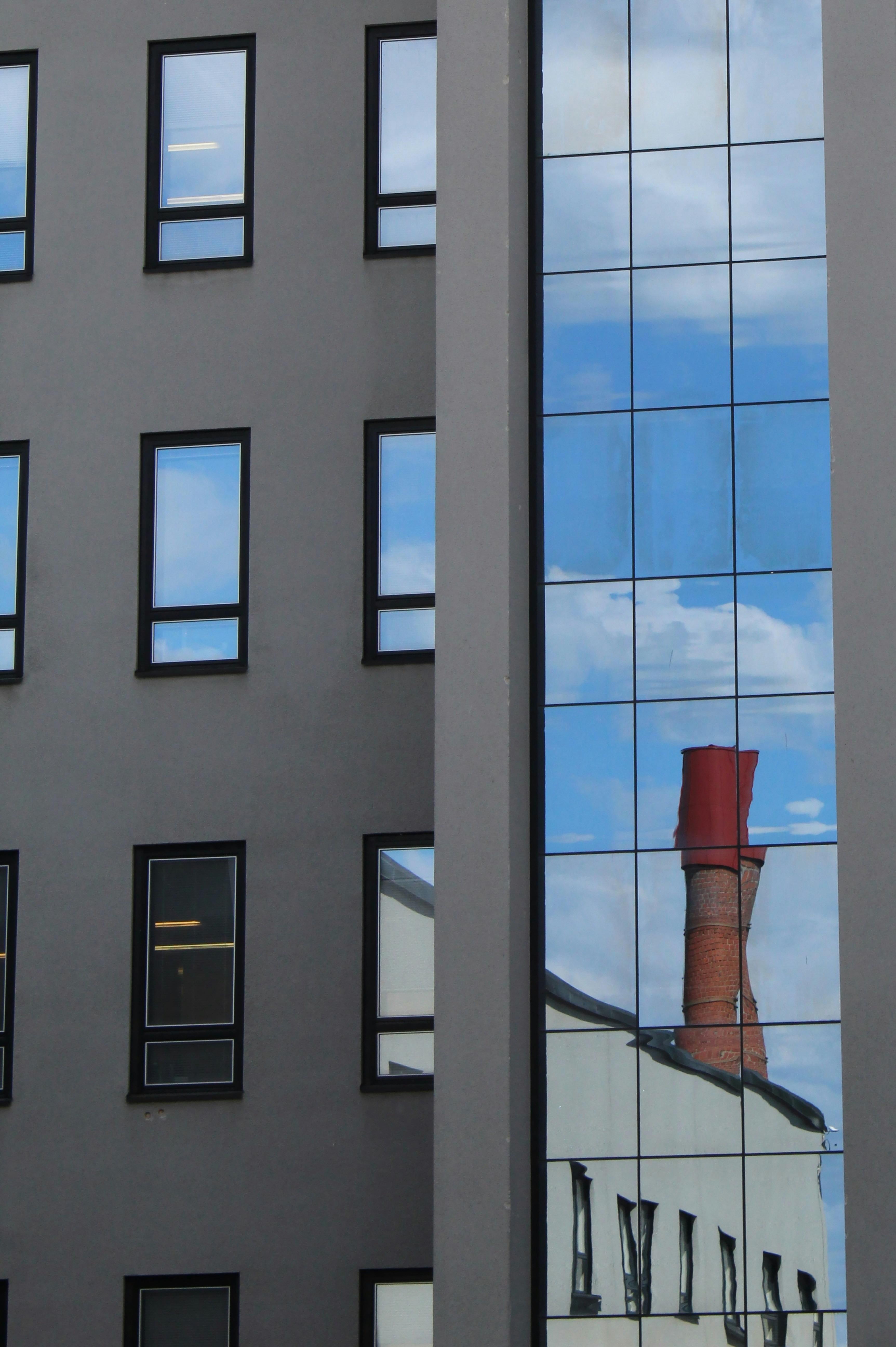 Glass Ribbon Reflects Sky and Chimney in a Narrow Facade