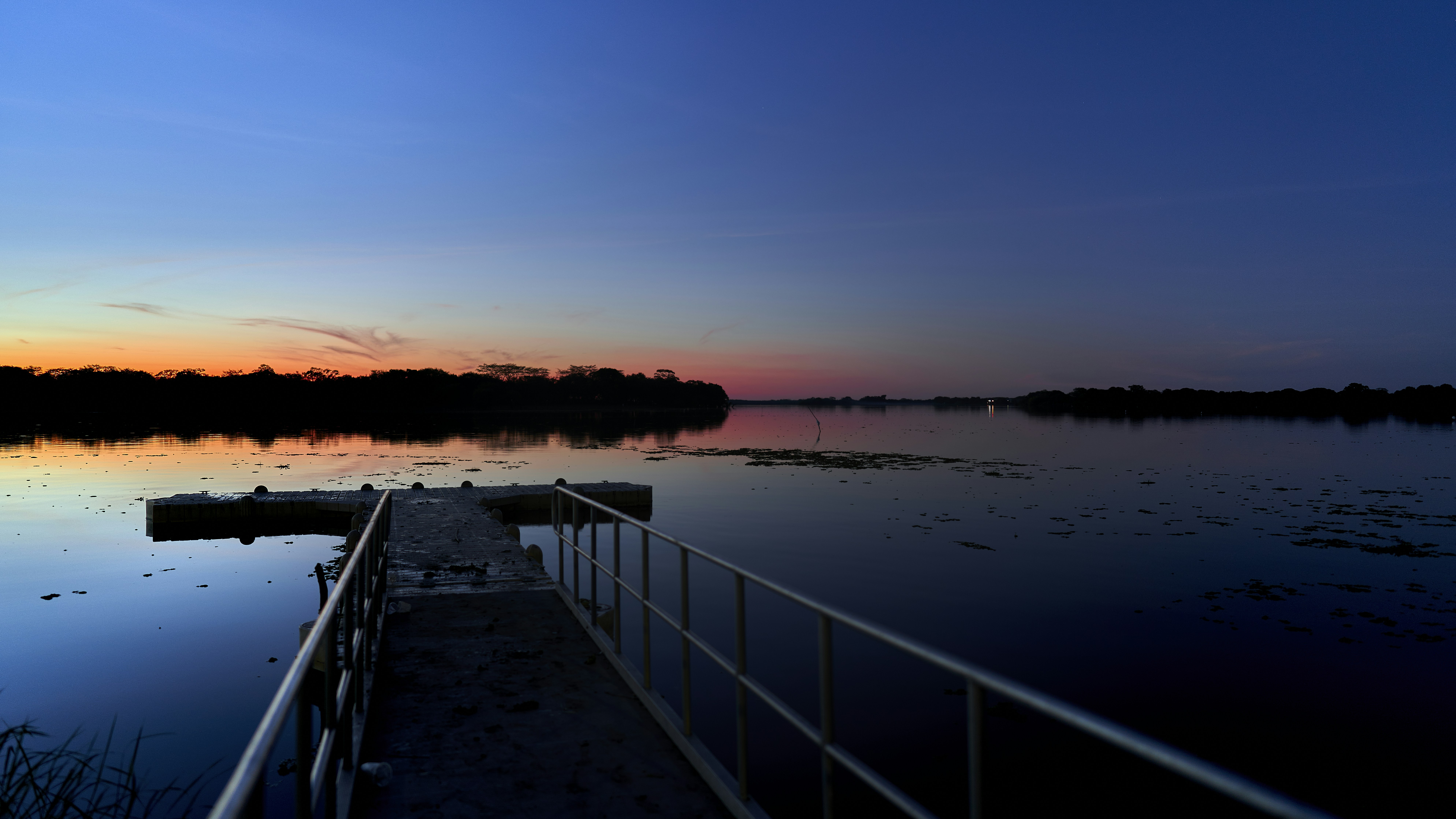 Dock extending into a calm lake under a twilight sky with vibrant hues of orange and blue.