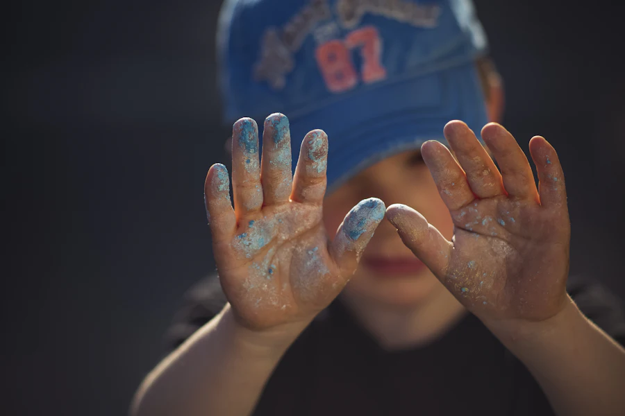 Child's hands covered in colorful paint, held up in a playful gesture, with a blurred background emphasizing creativity.