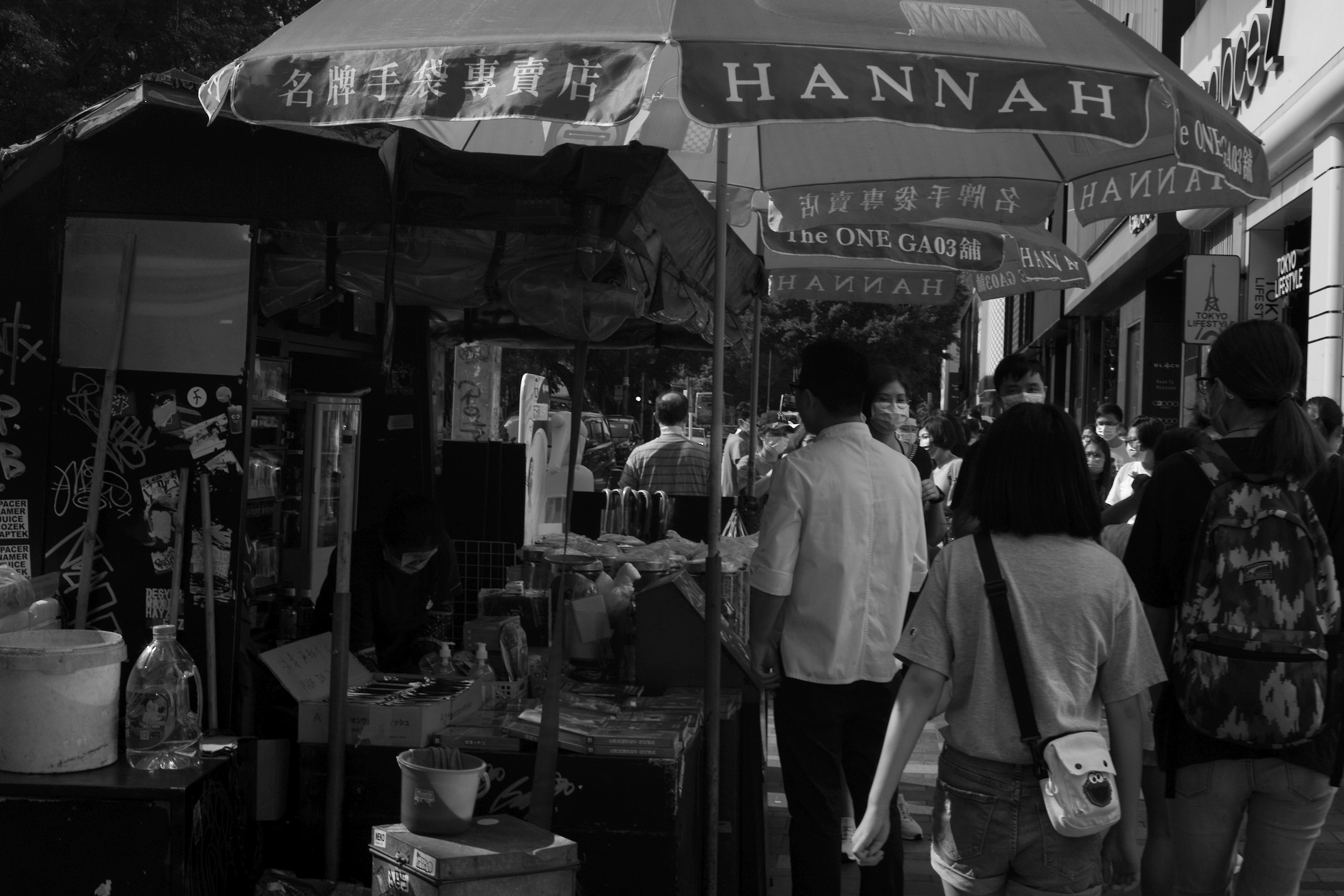 Bustling street market scene featuring vendors and shoppers navigating through stalls under colorful umbrellas.