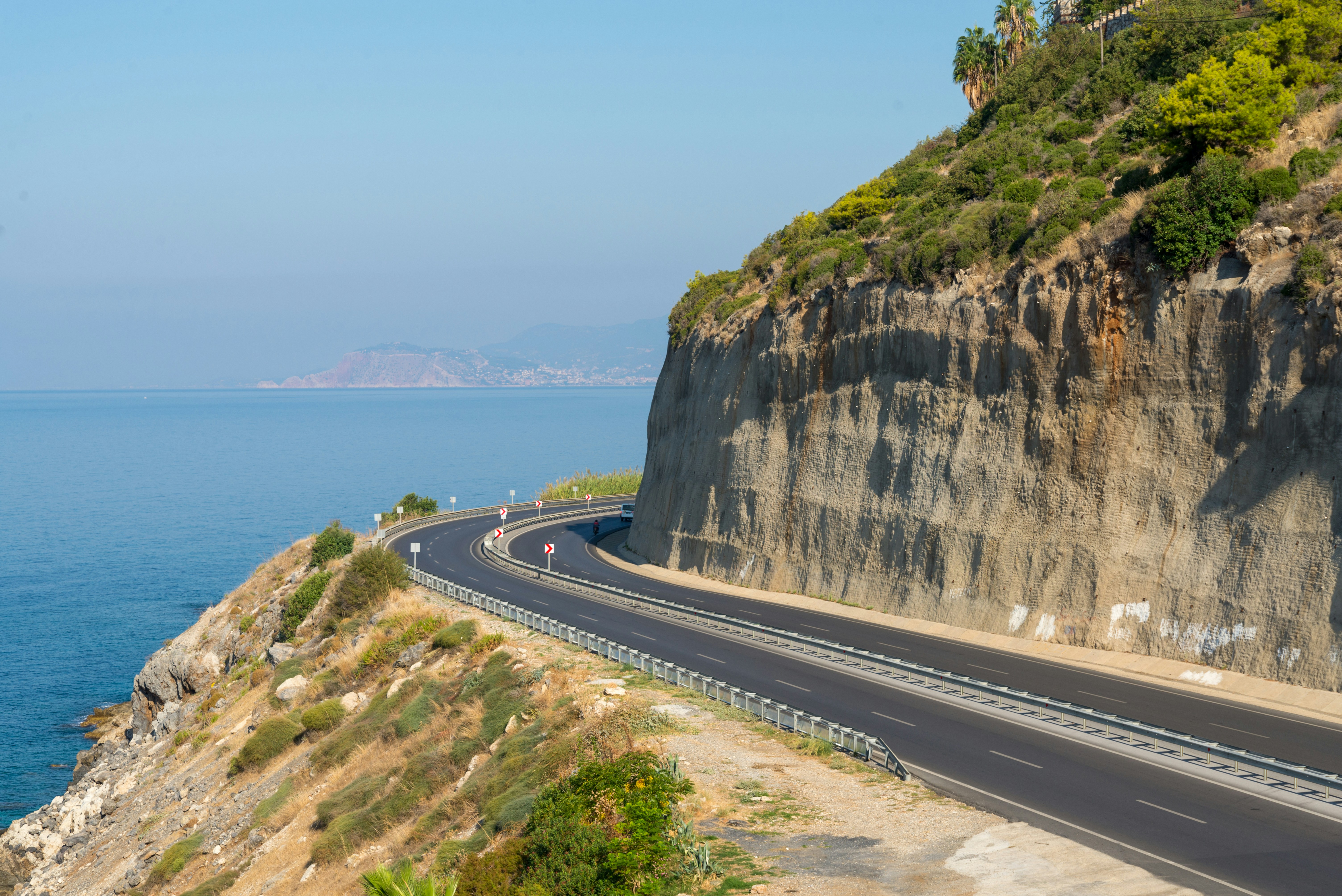 Winding road hugging a steep cliffside with blue ocean horizon in the distance.