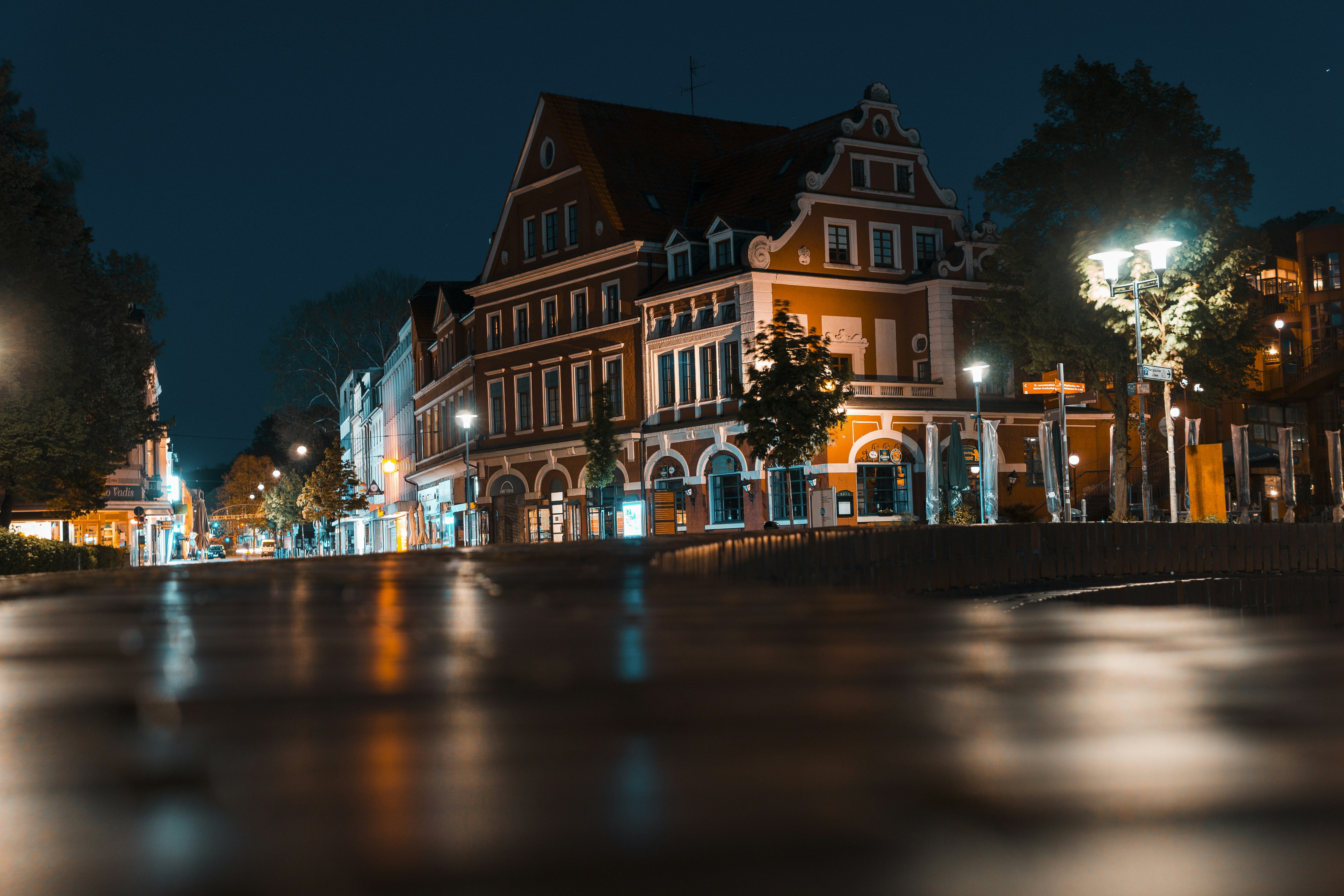 Historic building illuminated by streetlights, reflecting on wet pavement in a tranquil nighttime cityscape.