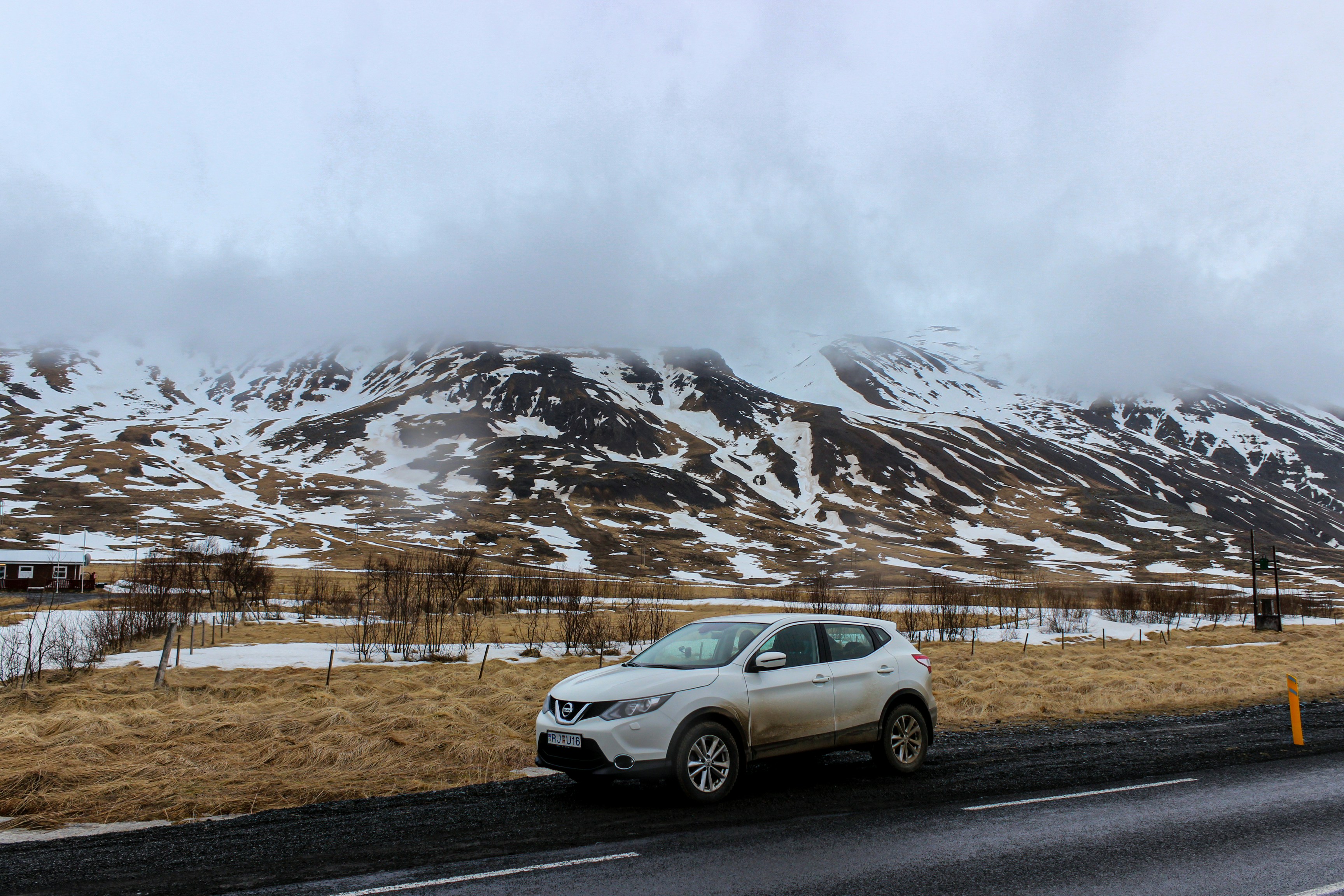 Silver SUV on a rain-washed highway beneath snow-dusted peaks
