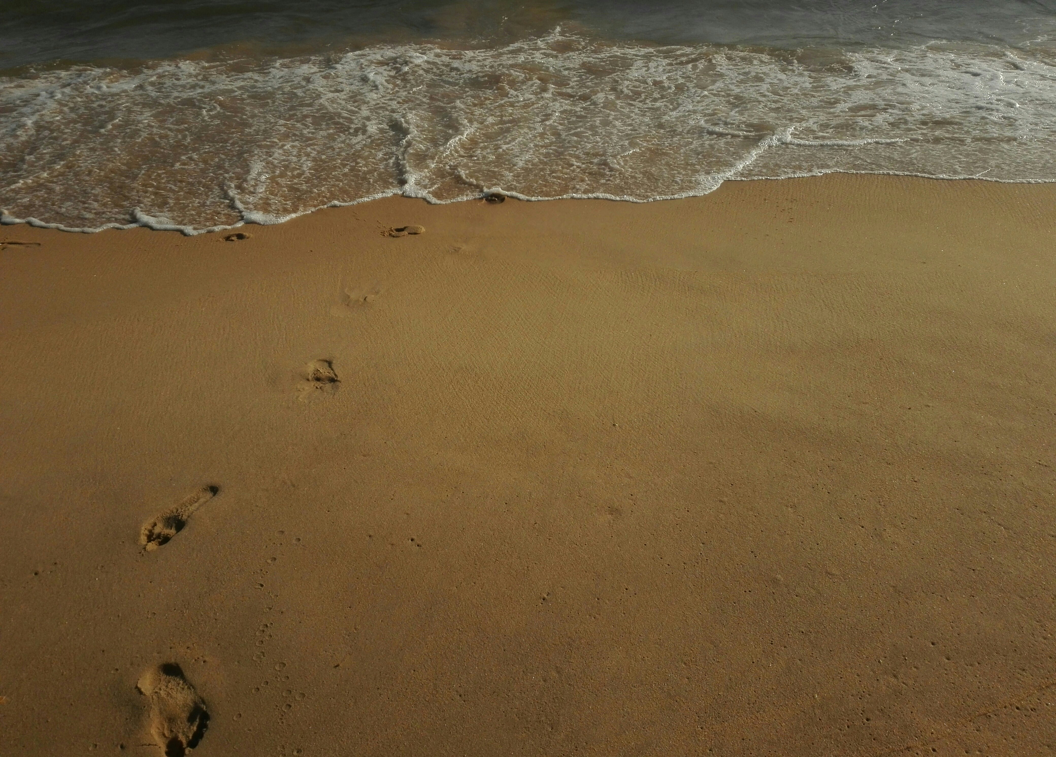 Footprints trail across golden sand leading to gentle waves lapping at the beach, evoking a sense of peace and solitude.