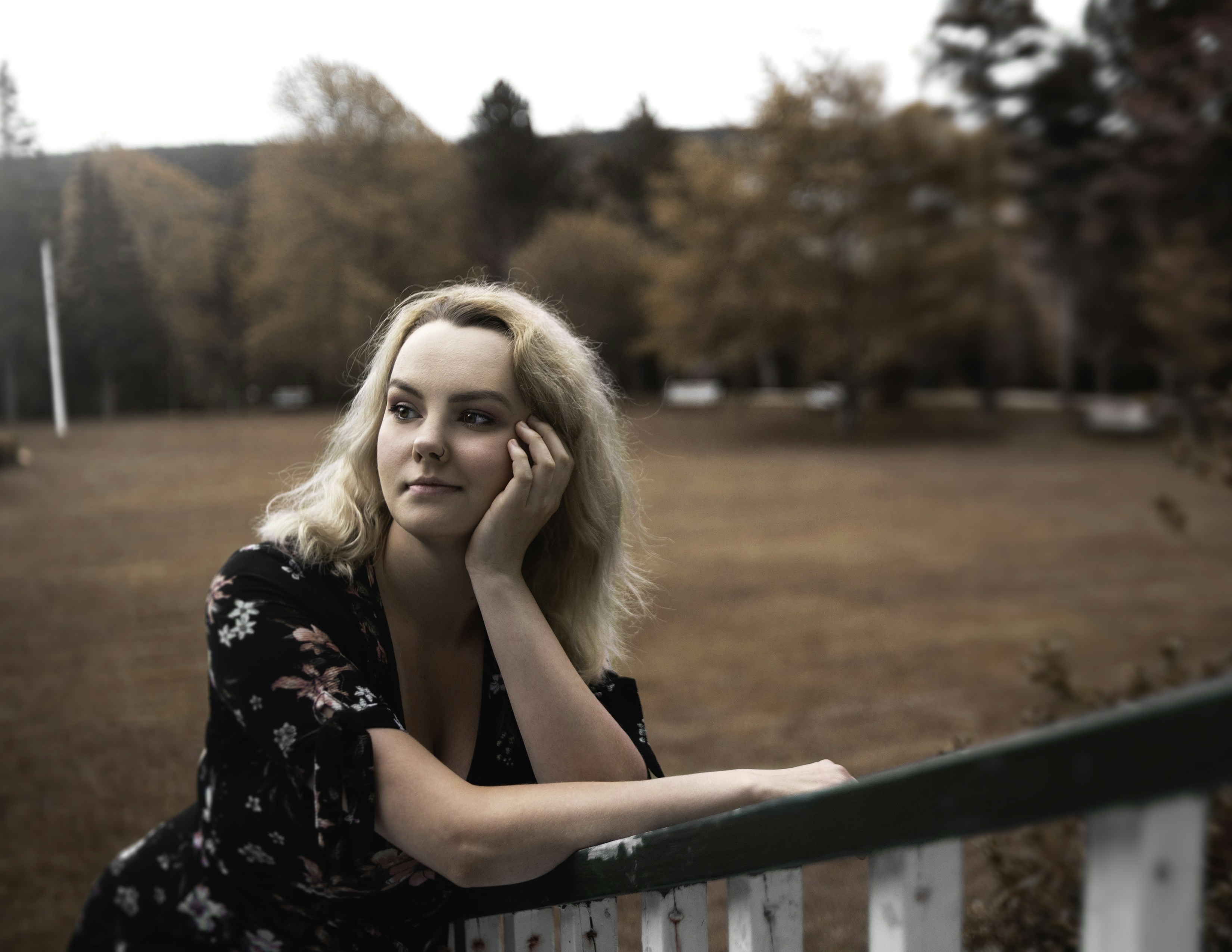 woman in black and white floral dress leaning on blue wooden fence during daytime