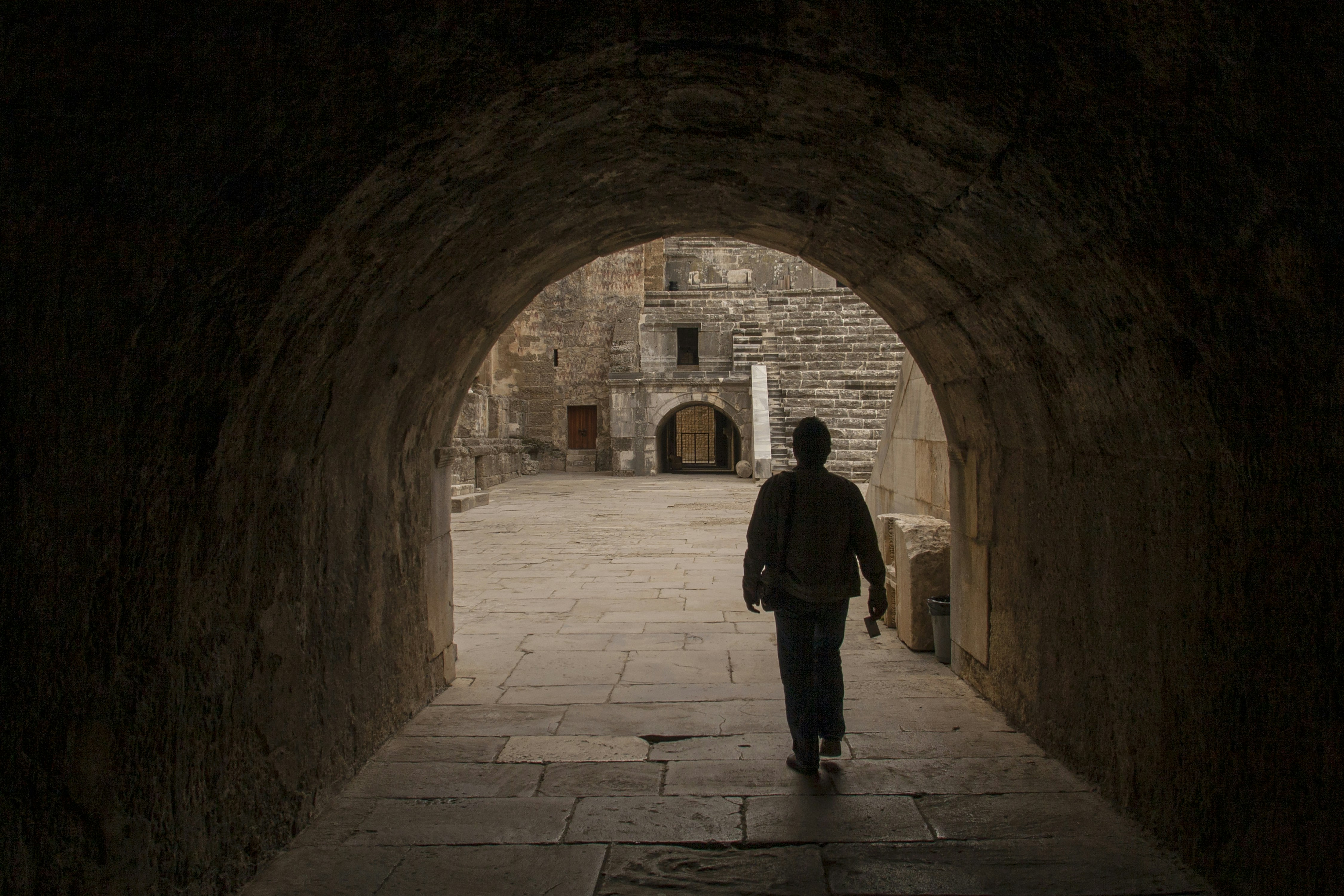 The entry archway into Aspendos Theater, a marvelously well-preserved Roman Theater in southern Turkey. | man in black jacket standing on brown brick hallway