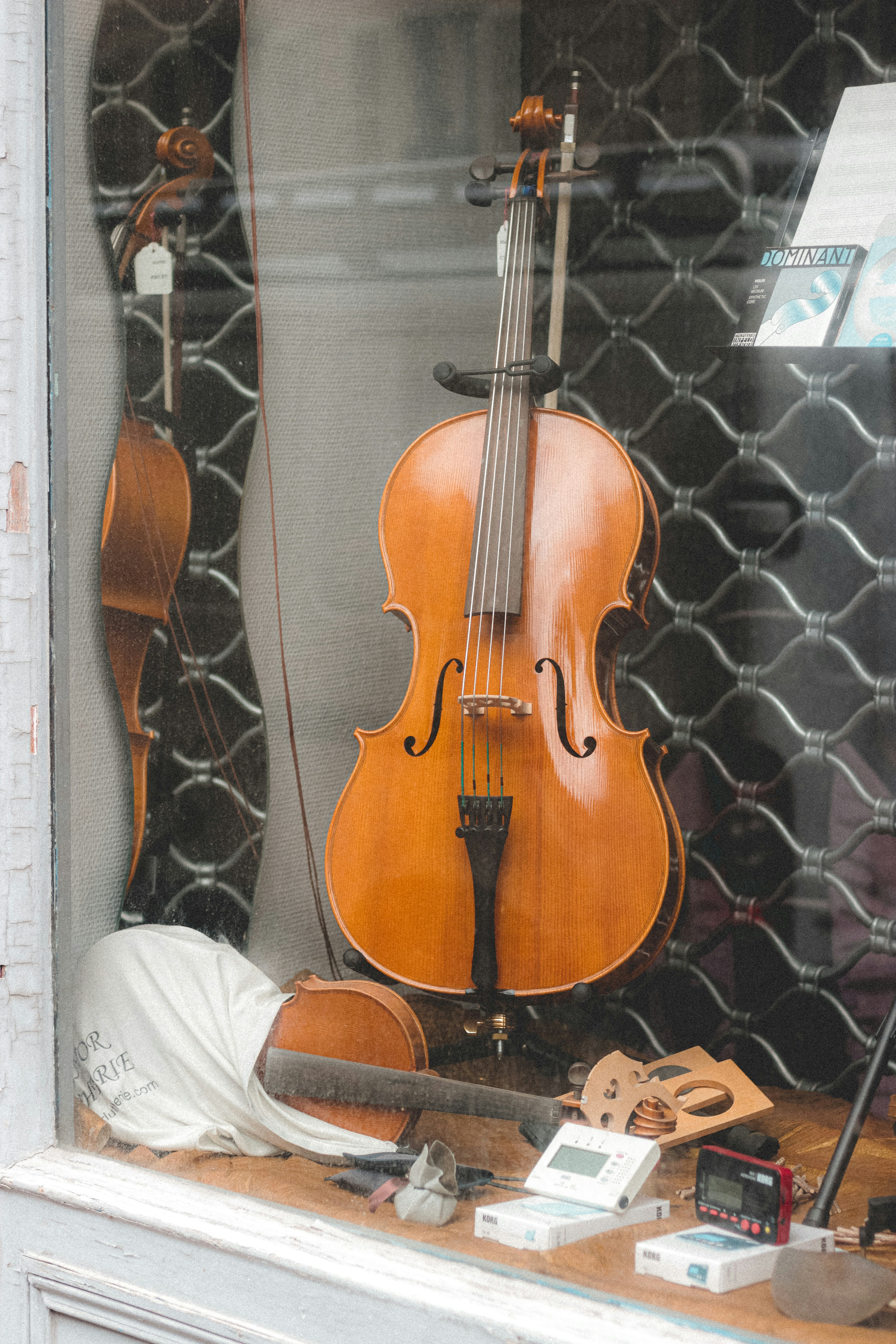 A beautifully crafted violin stands prominently in a shop window, accompanied by a collection of musical accessories and a second string instrument in the background.
