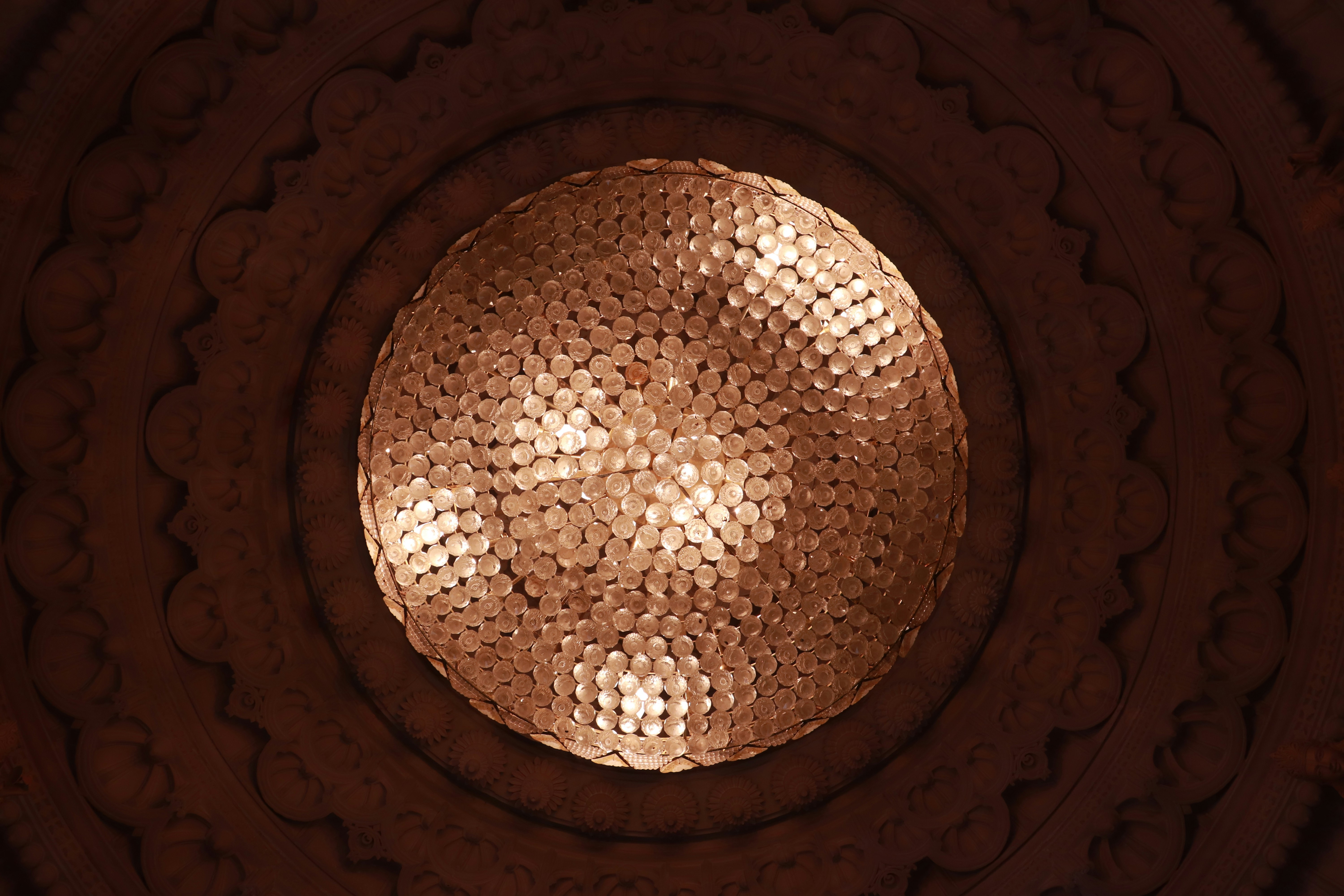 Intricate ceiling design featuring a circular arrangement of reflective elements, illuminated from above. The warm glow highlights the craftsmanship and details of the architecture.