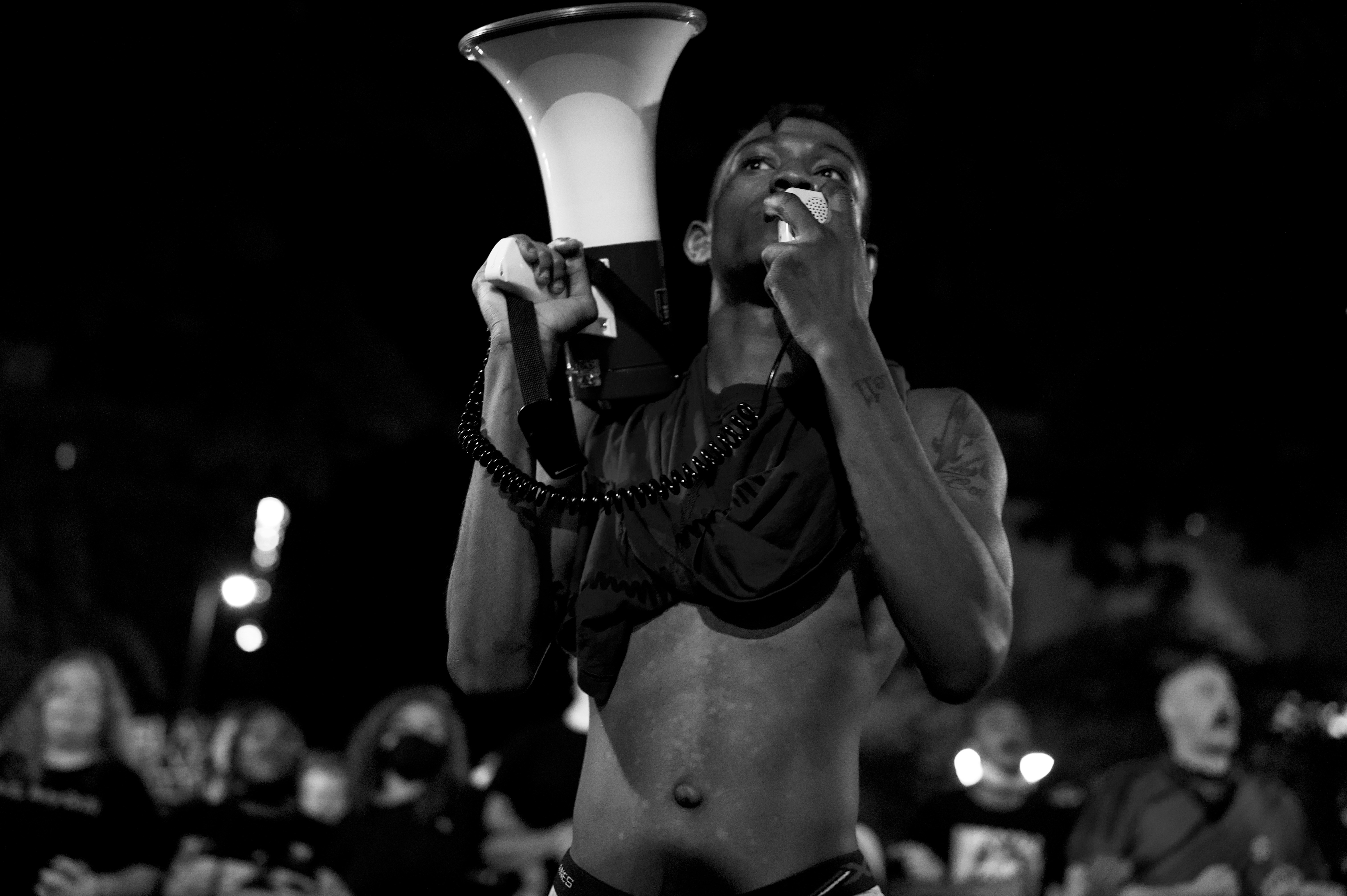 Midnight Chorus: A Shirtless Street Performer with Megaphone in Focus