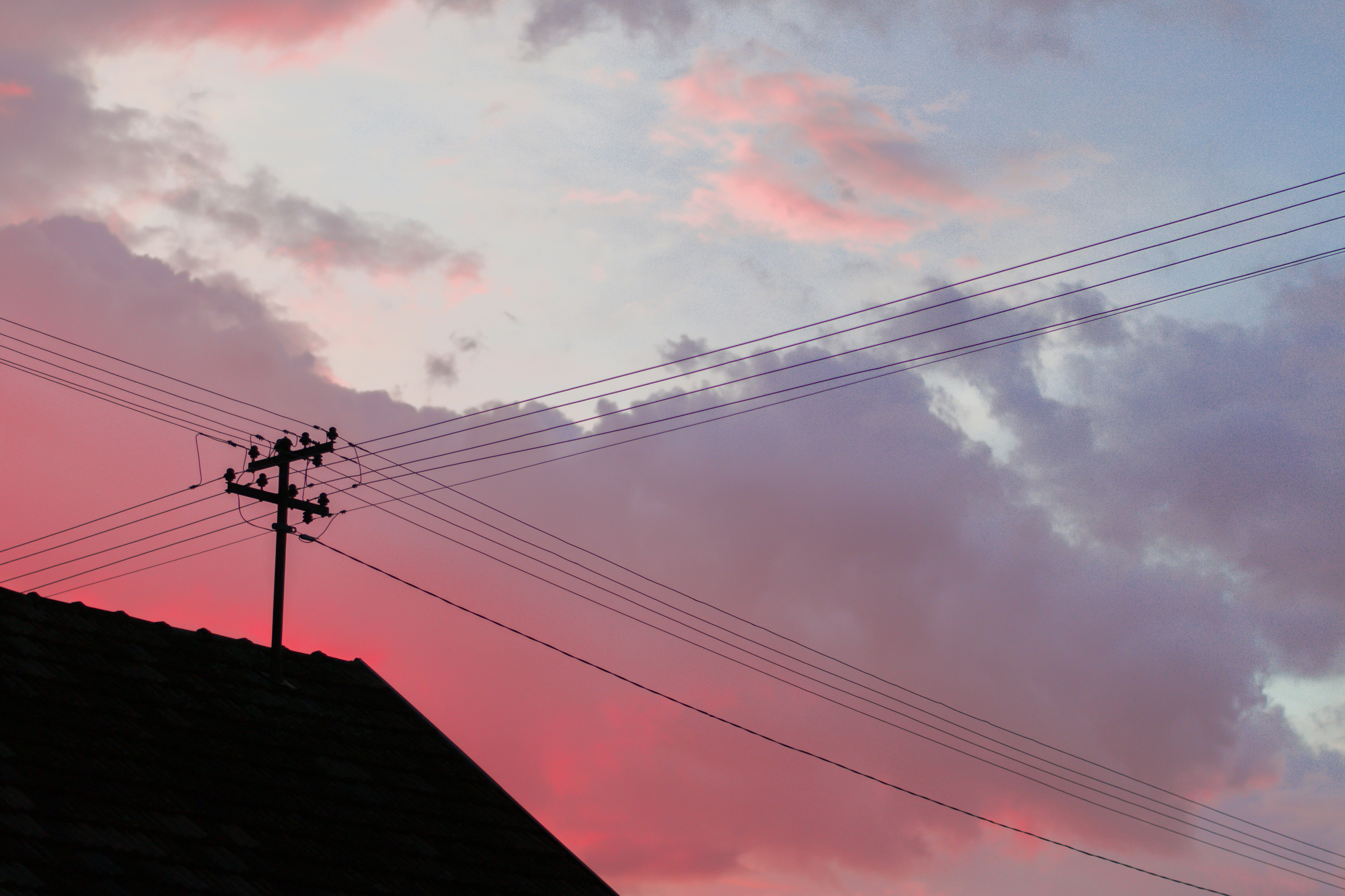 Silhouetted rooftop against a vibrant pink and blue sky, with power lines crisscrossing above. The scene captures the tranquil transition from day to night.