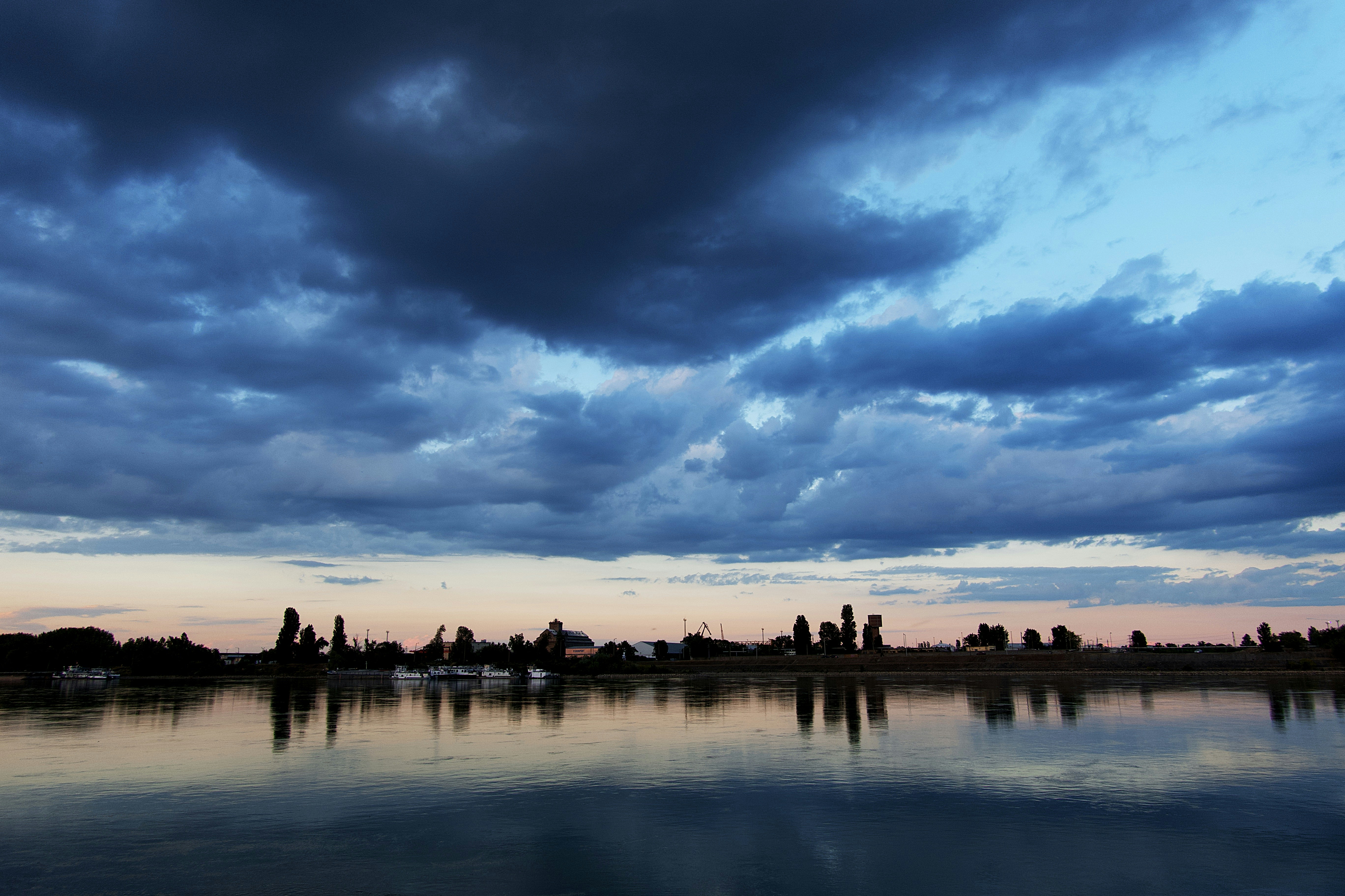 Silhouetted treeline mirrored in the tranquil Danube under dramatic evening clouds.