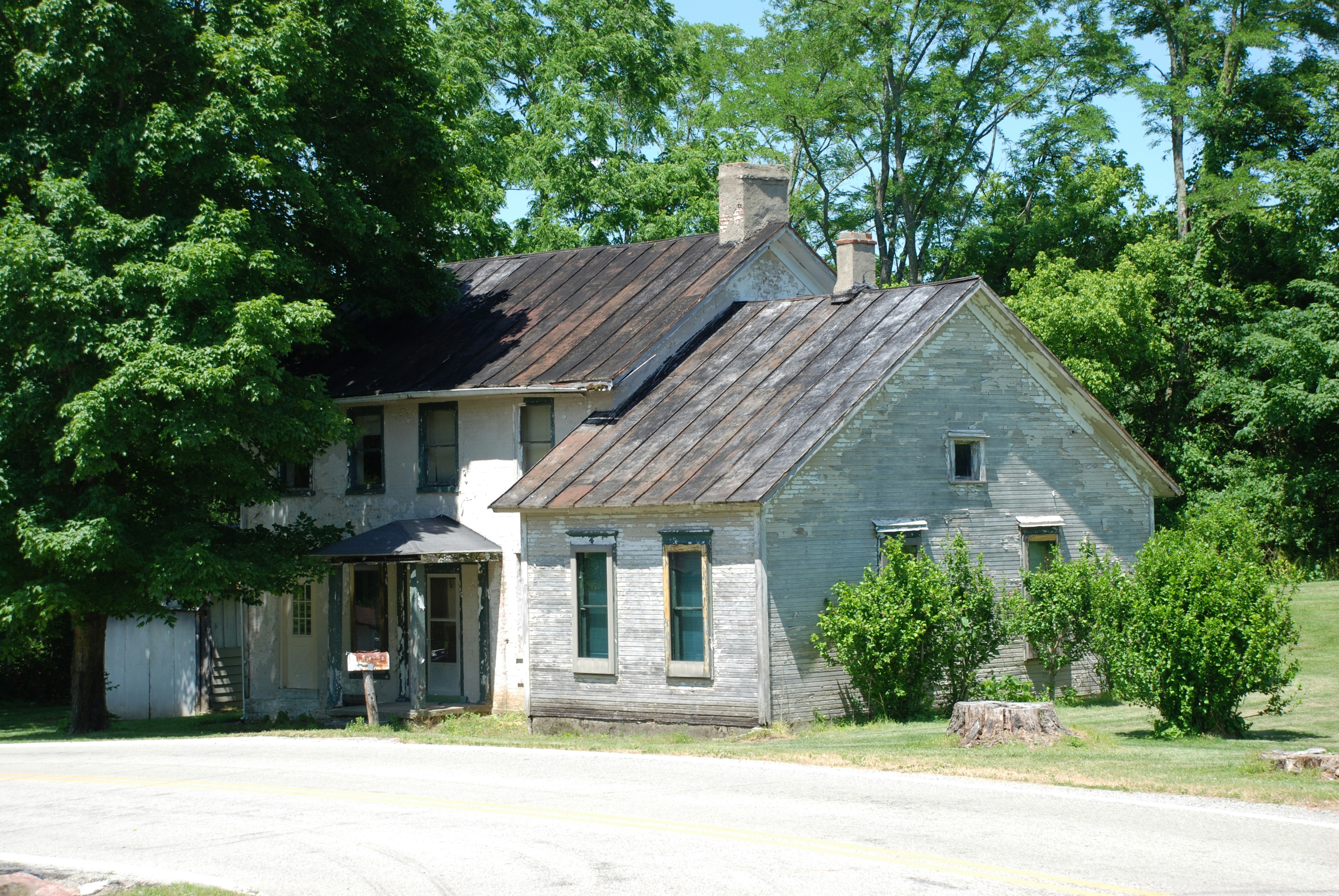 Weathered farmhouse surrounded by lush greenery, showcasing a blend of rustic charm and nature's reclamation.