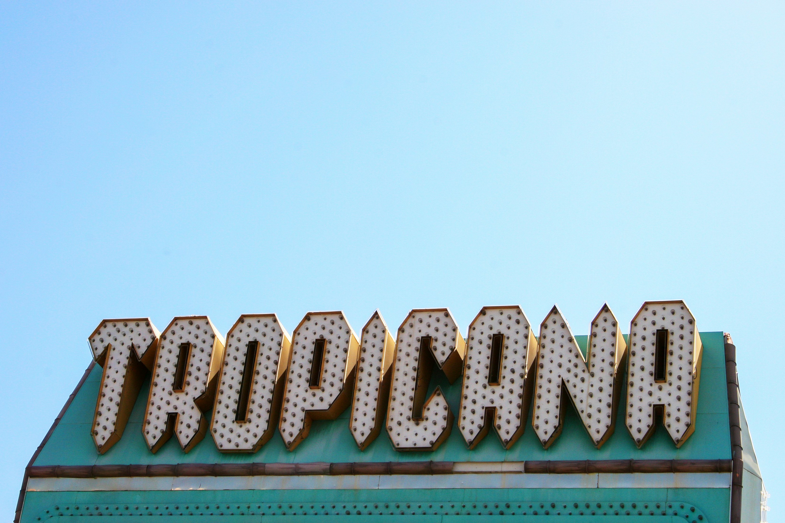Vintage Tropicana sign adorned with bright lights against a clear blue sky, showcasing retro design elements.
