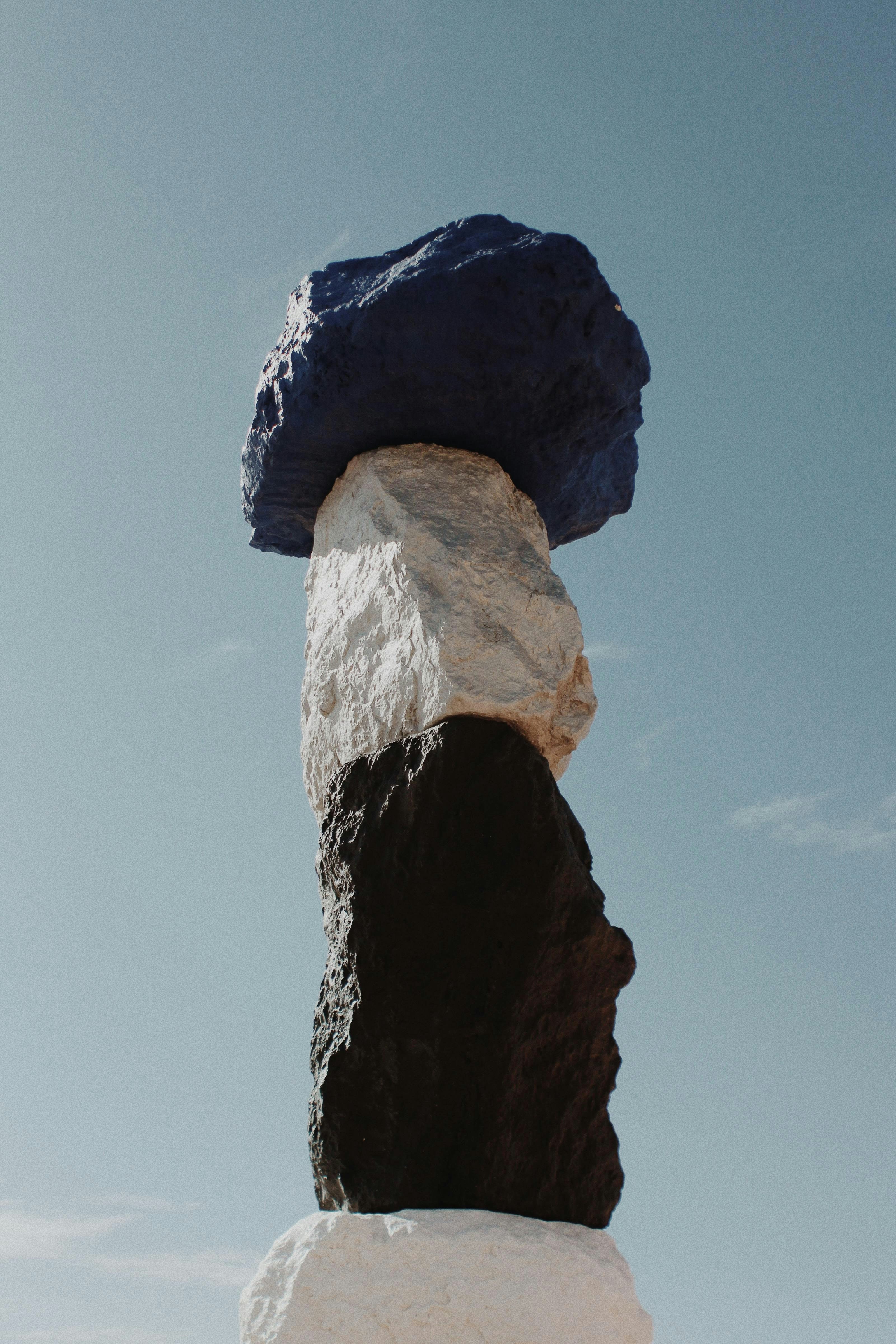 A towering stack of painted rocks in vibrant colors against a clear blue sky, showcasing an artistic blend of nature and human creativity.