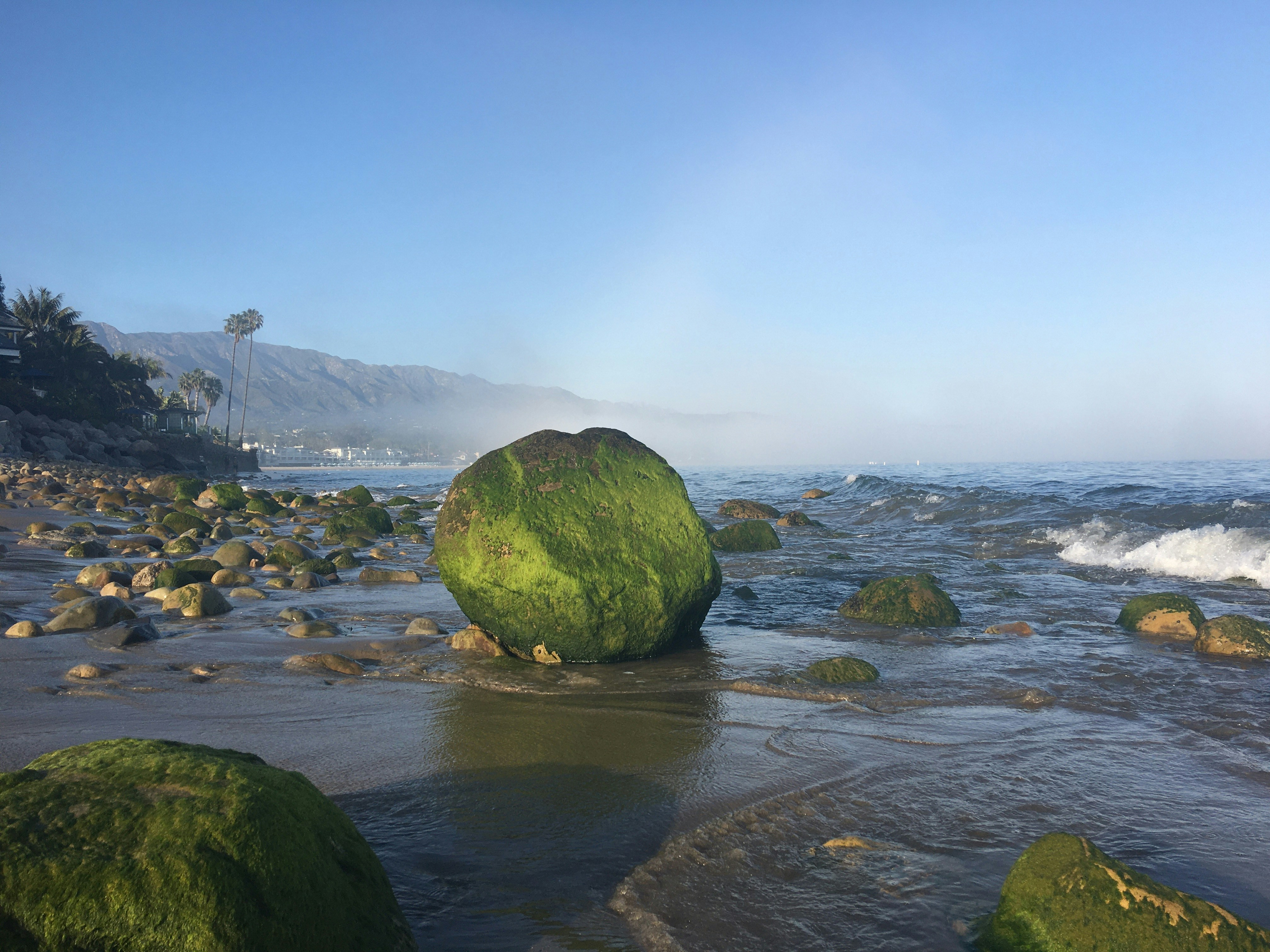 green rock formation on body of water during daytime