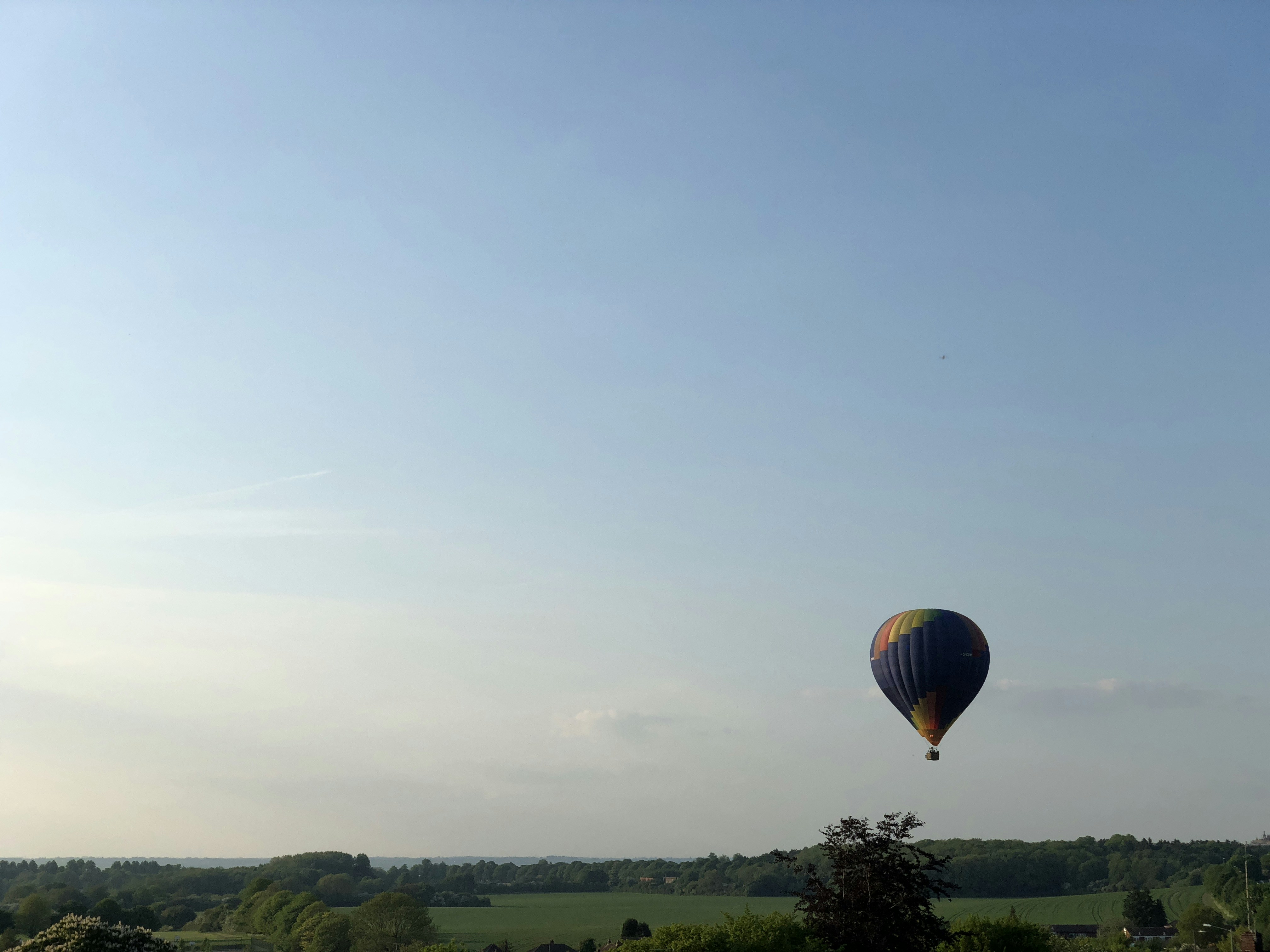 A vibrant hot air balloon drifts gracefully over lush green fields under a clear sky.