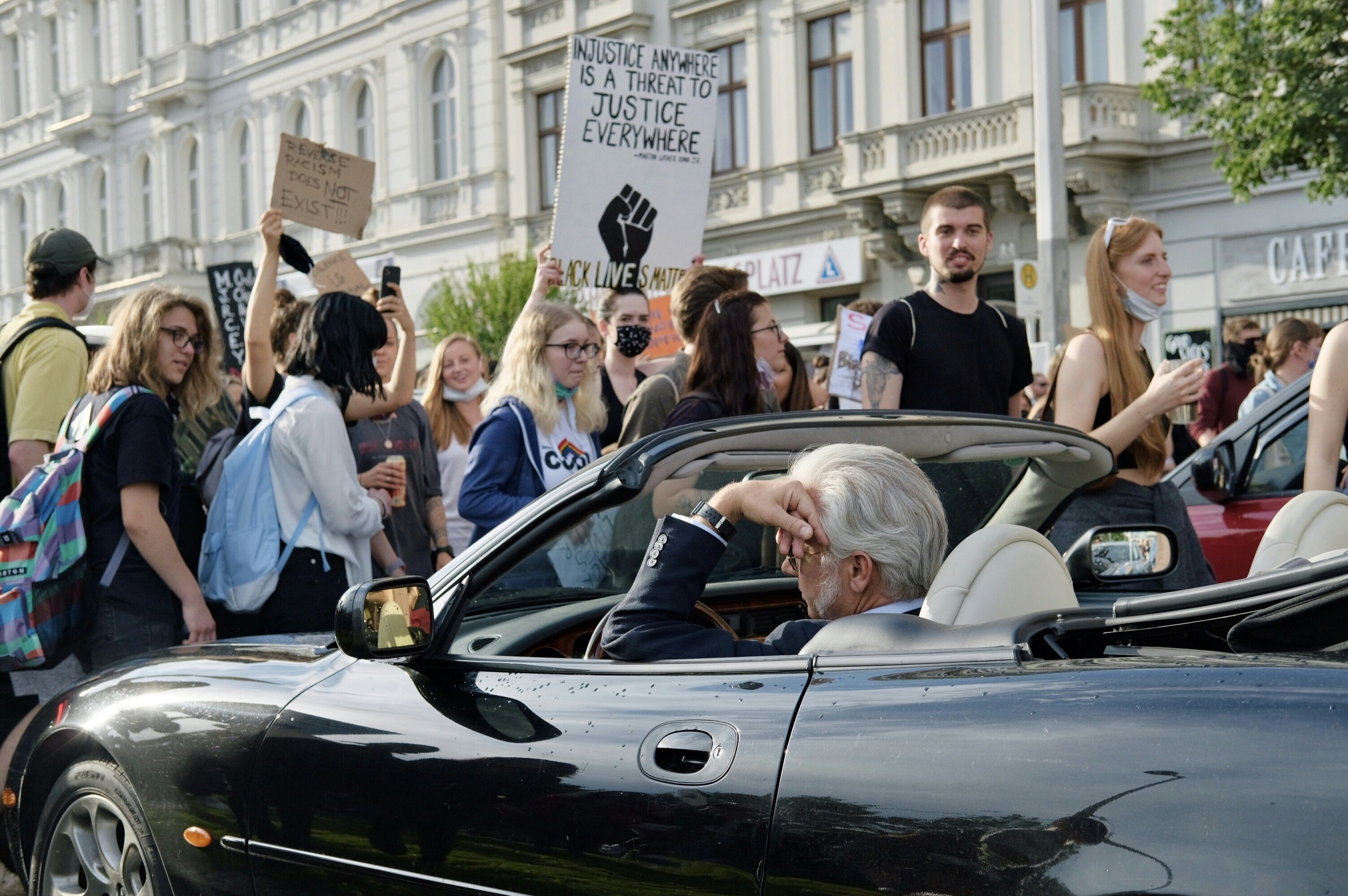 Convertible in the Crossfire: A Street Rally Framed by Protest Signs