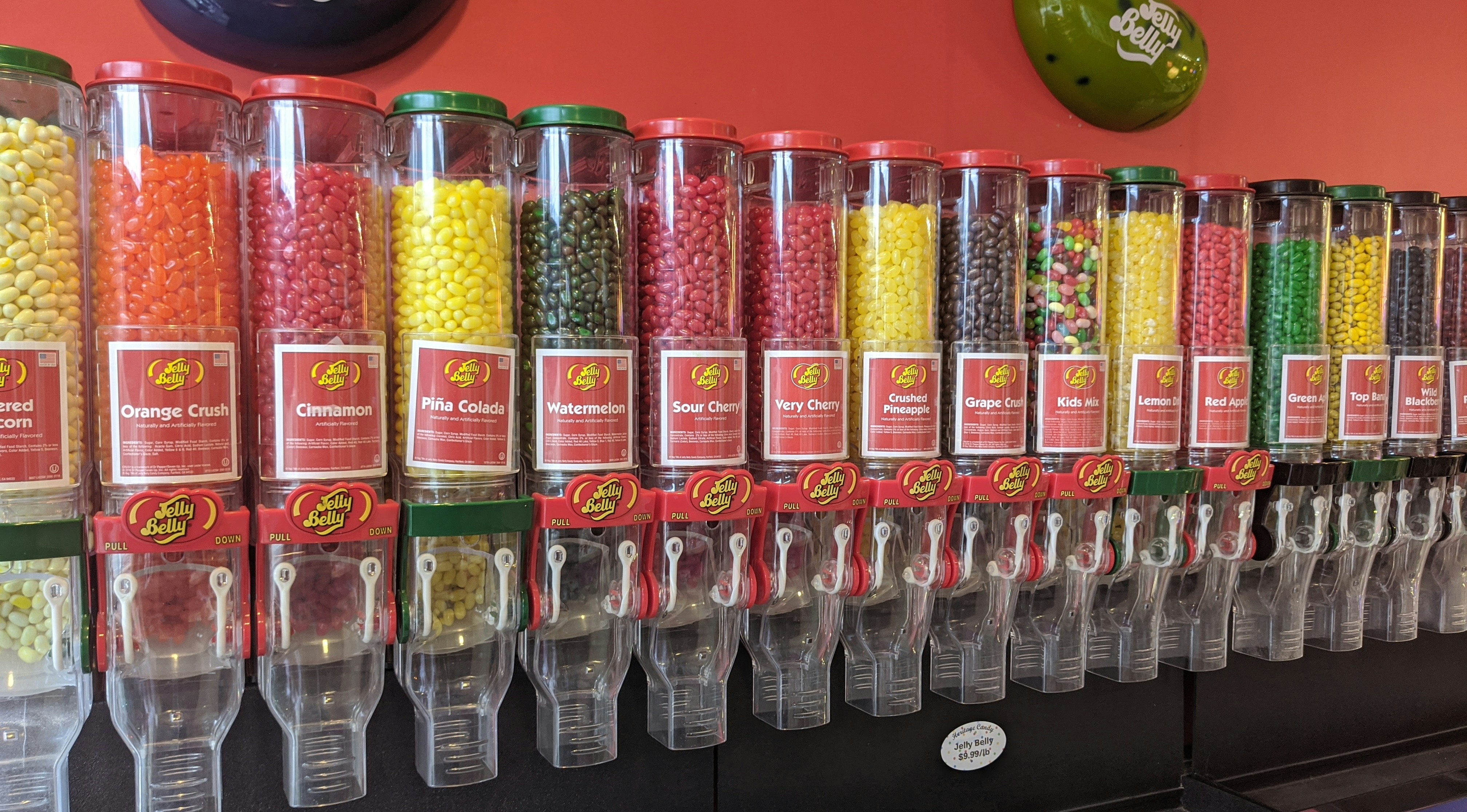 Row of transparent candy dispensers filled with colorful gumballs against a warm red wall, forming a vibrant display.