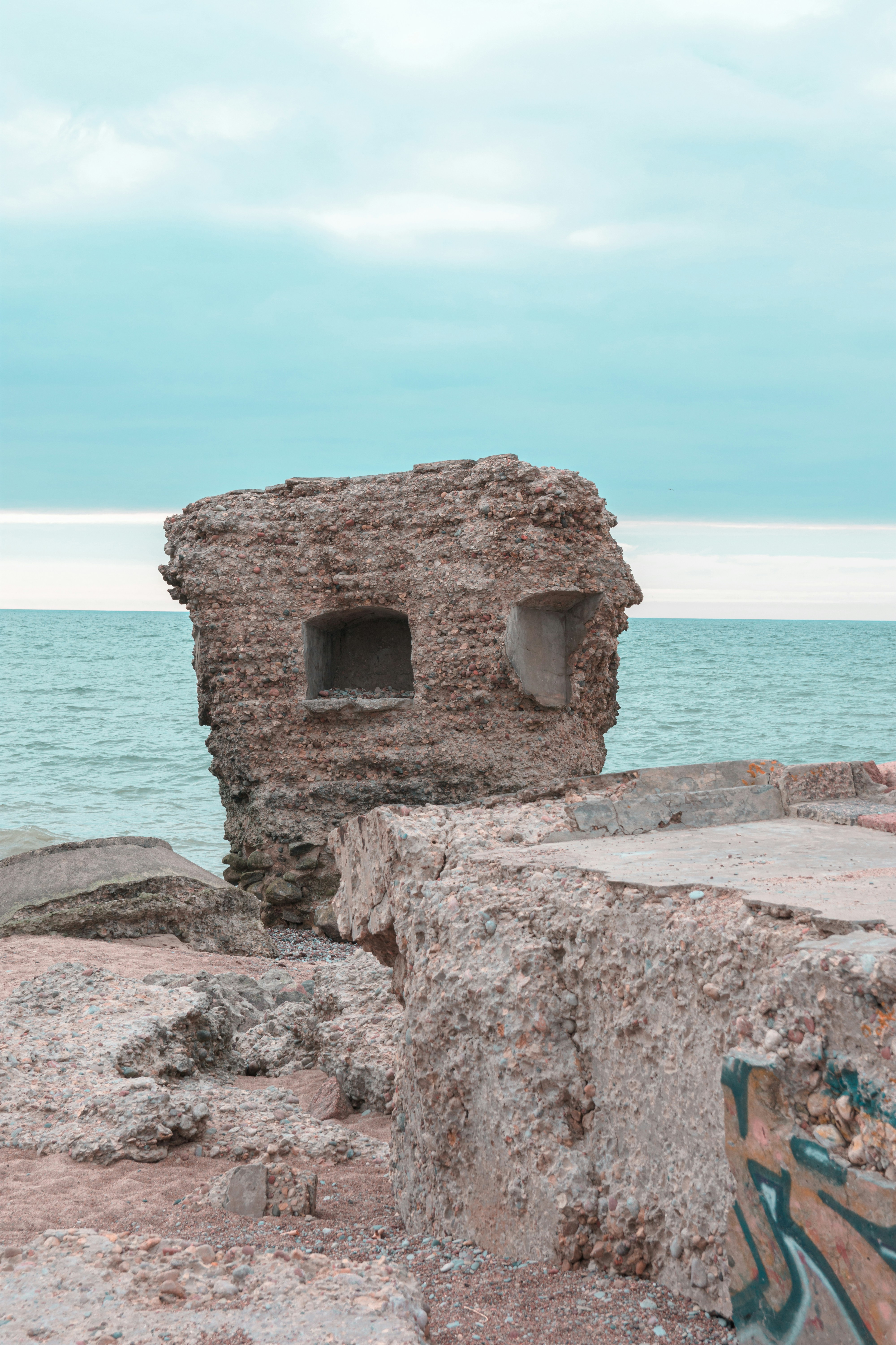 Weathered stone structure with hollowed openings stands against a tranquil seascape under a cloudy sky.