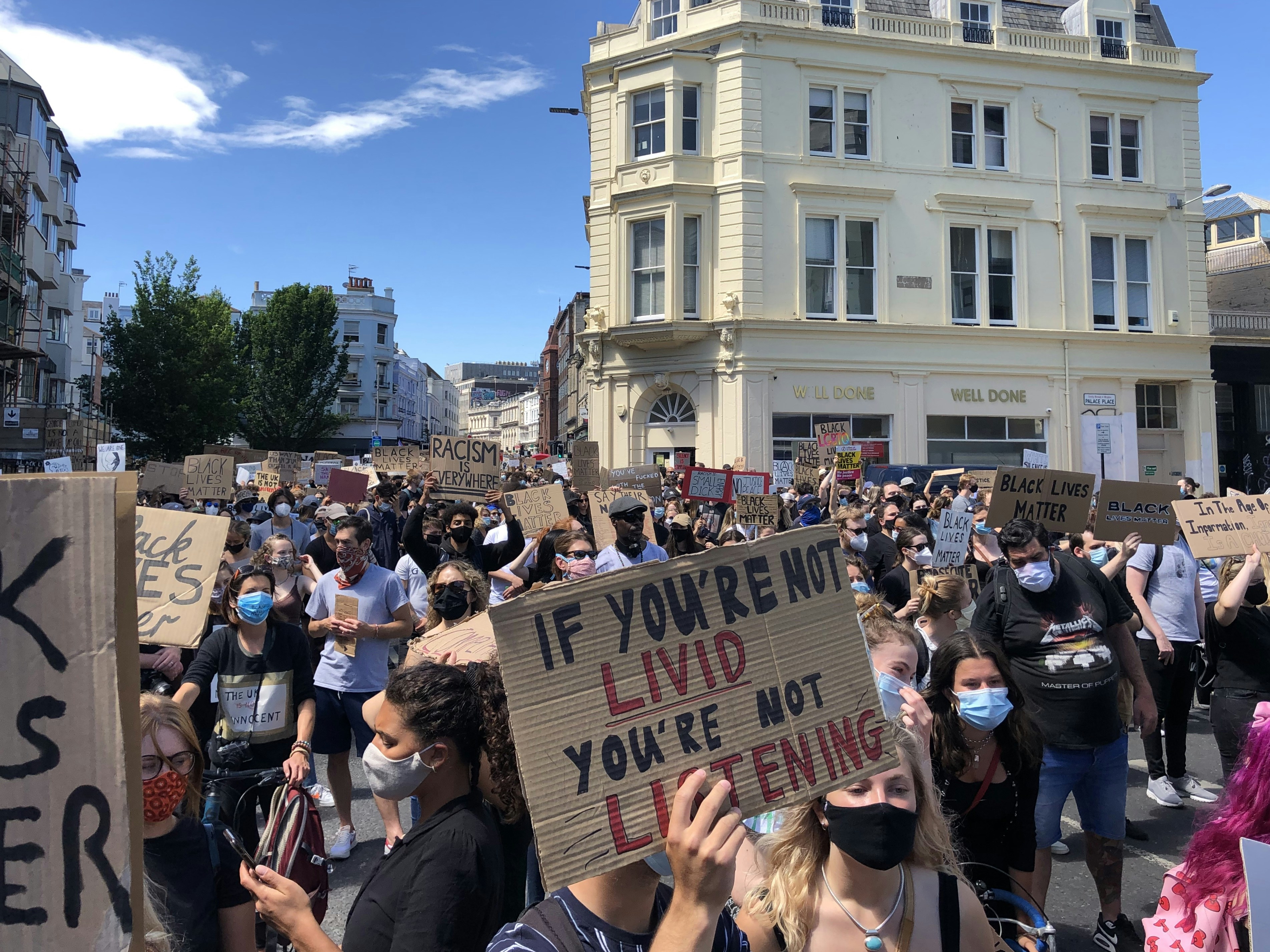 Crowd of protesters holding signs advocating for racial equality during a demonstration, with buildings in the background.