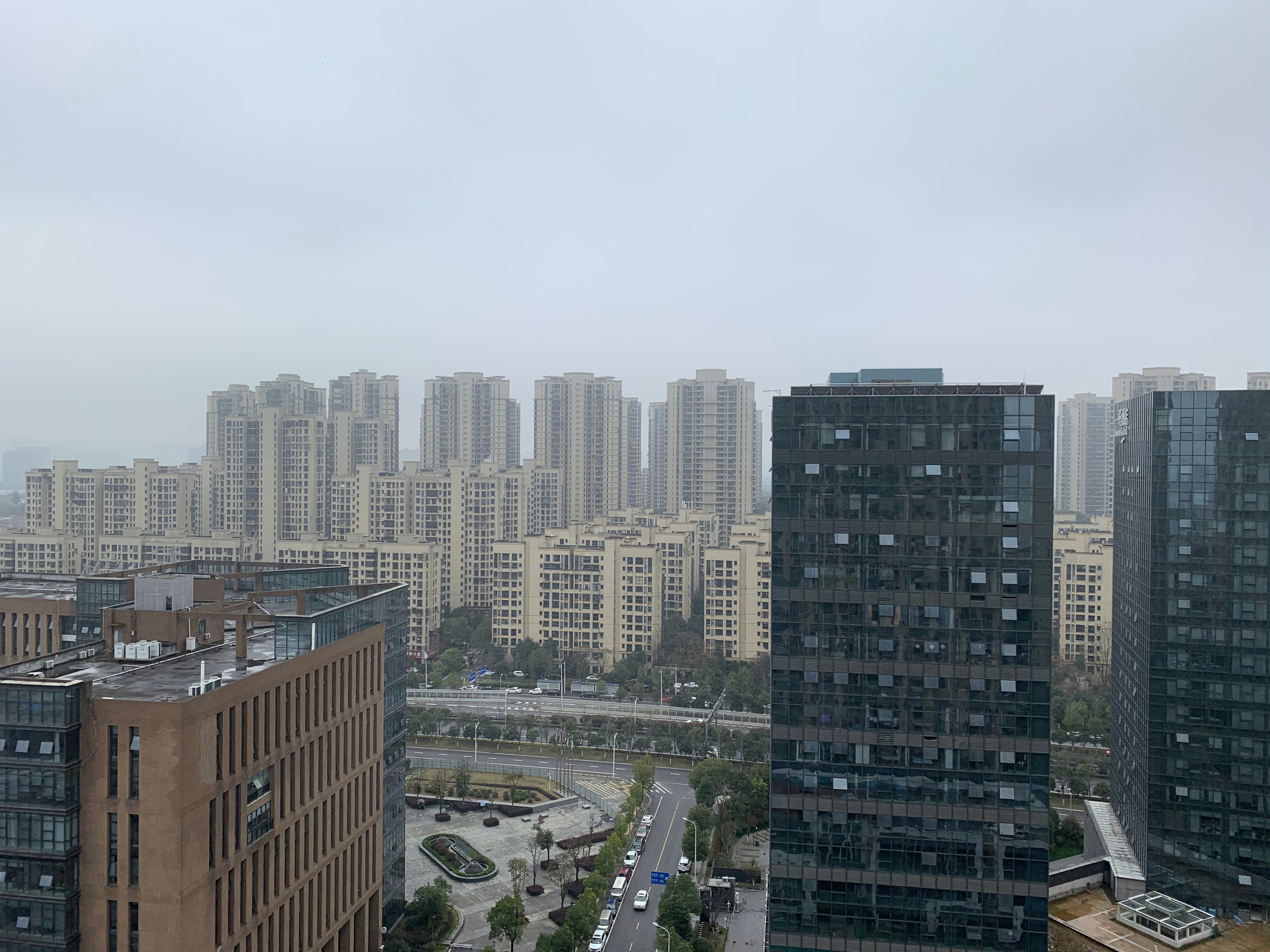 A panoramic view of a modern city skyline featuring a mix of high-rise buildings under a cloudy sky. The architecture showcases a blend of contemporary styles.