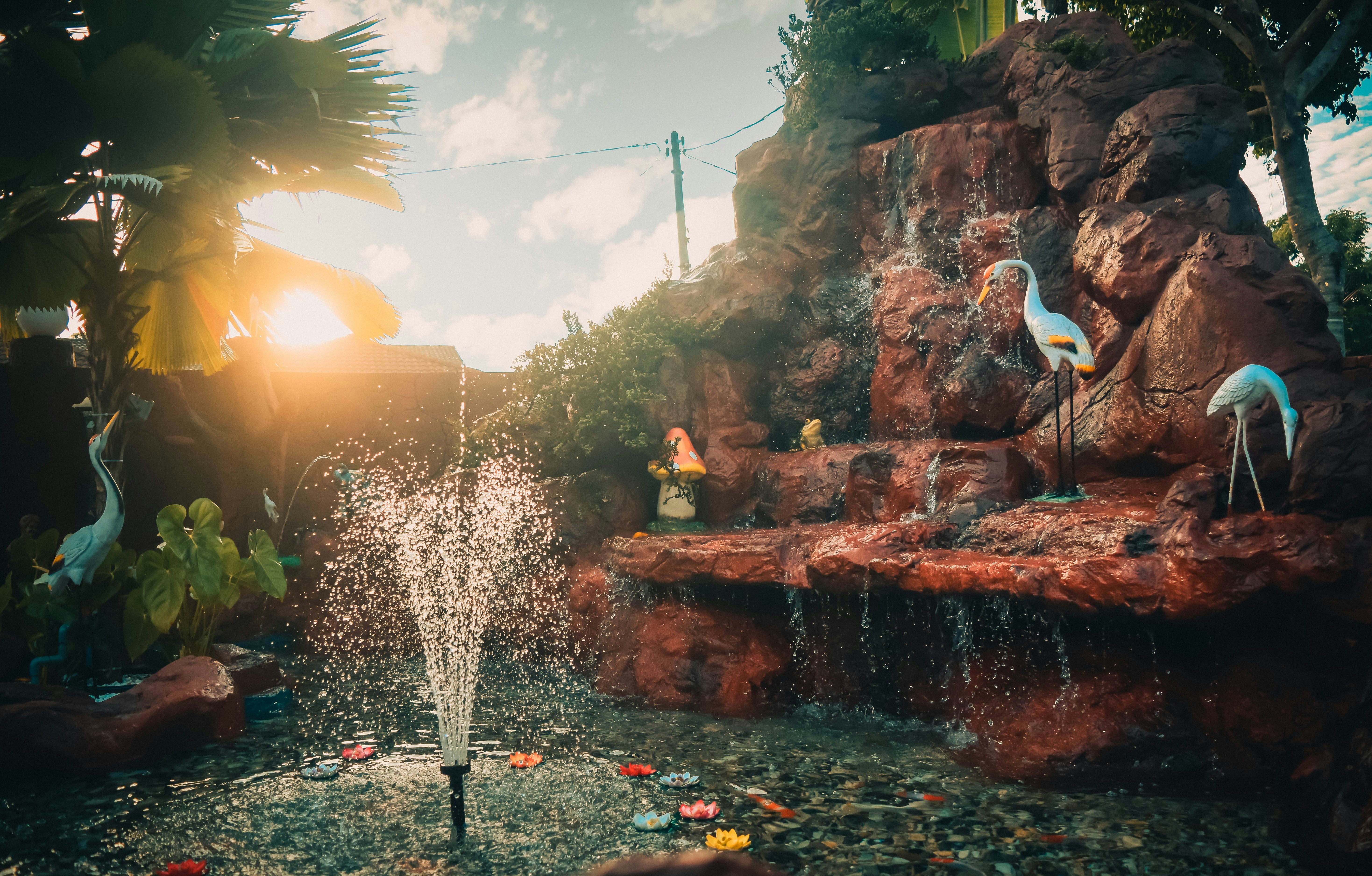 A tranquil garden fountain surrounded by vibrant flora and whimsical sculptures, illuminated by the warm glow of the setting sun.