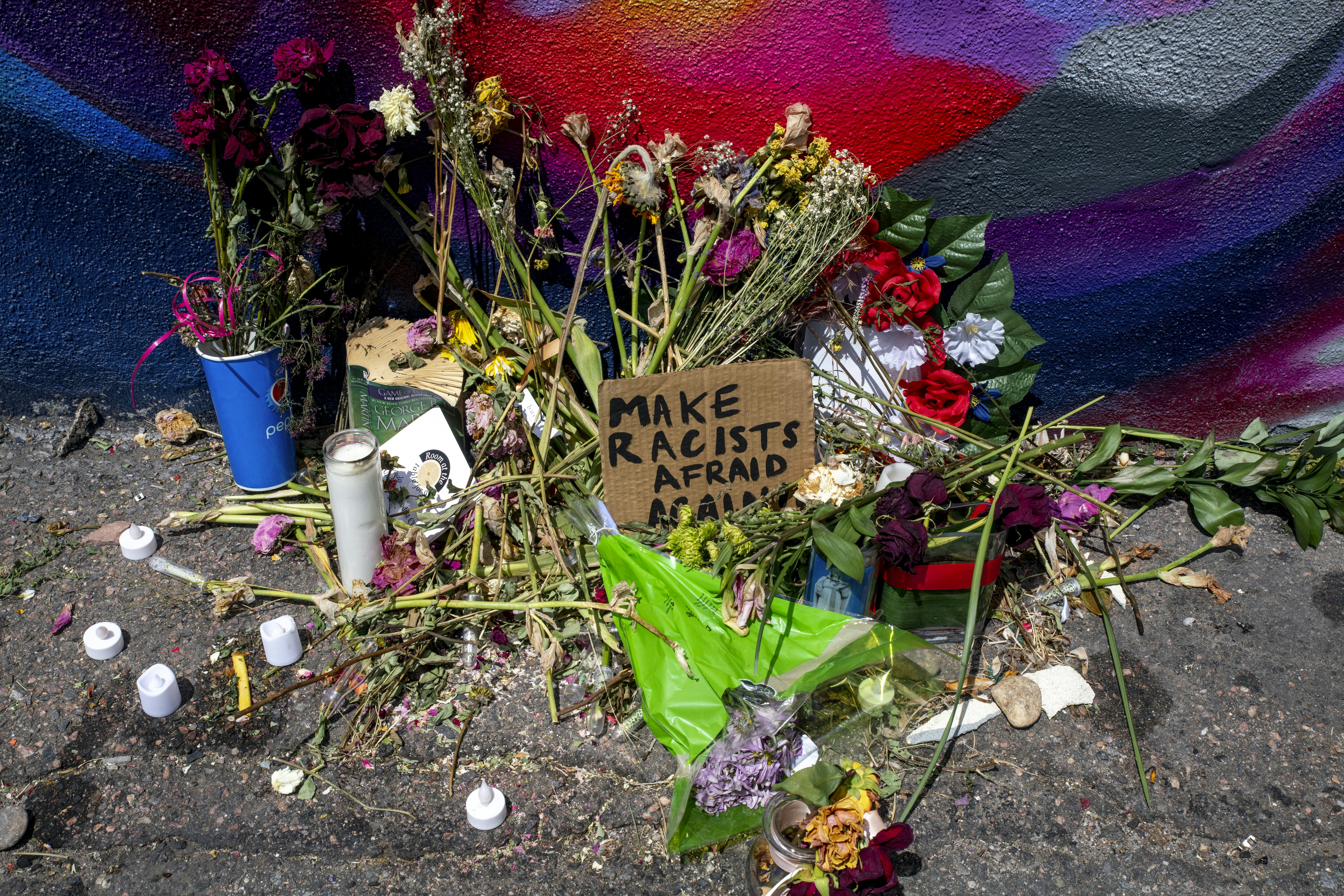 Flowers, votive candles, and a hand-painted sign spreading a message amid a graffiti backdrop