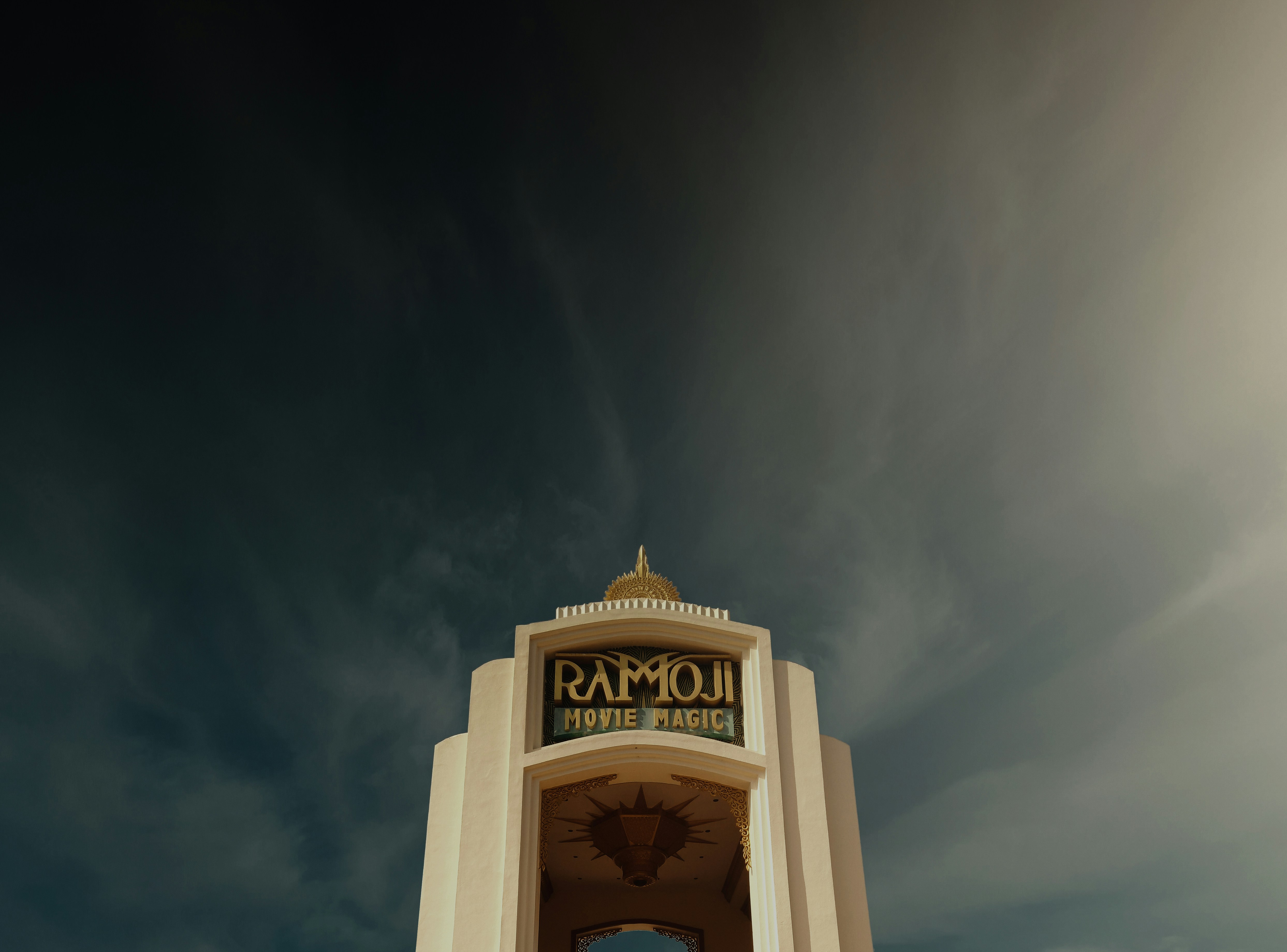 Monumental archway with 'Ramoji Film City' sign under a dramatic sky.