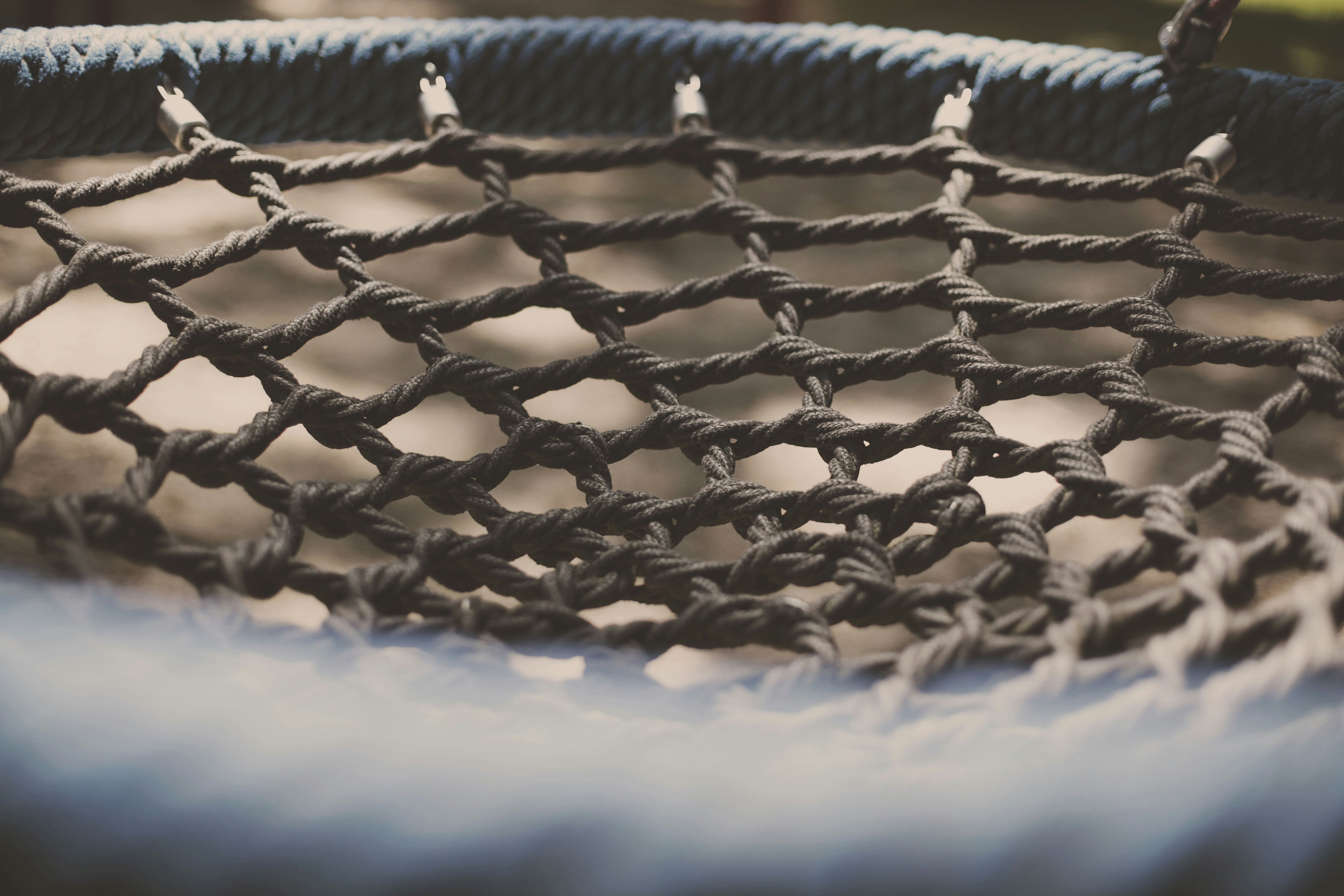 Close-up of a textured rope net, showcasing intricate knots and patterns. The image highlights the interplay of light and shadow on the fibers.