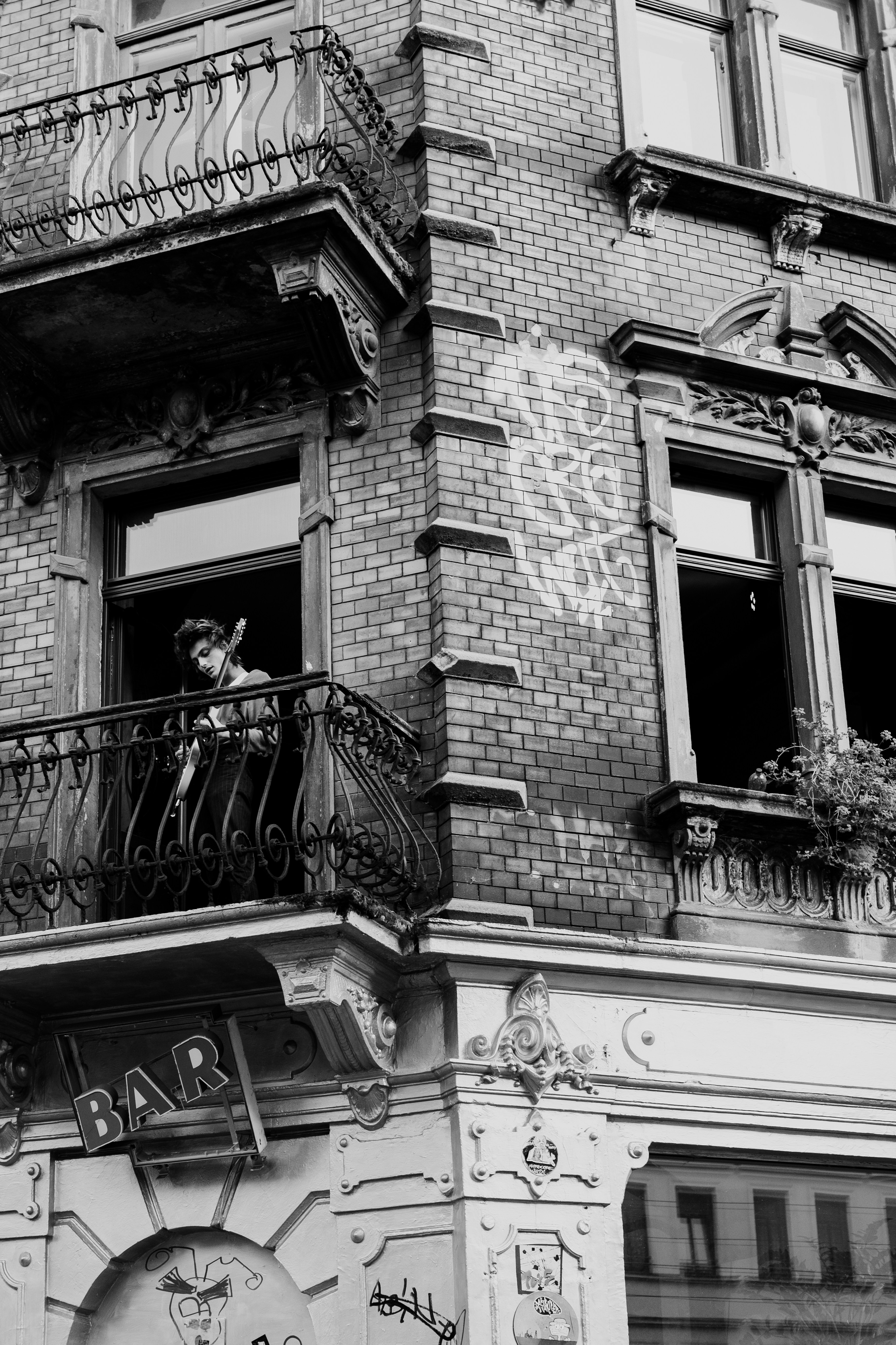 Guitarist on a Wrought-Iron Balcony Against Brickwork