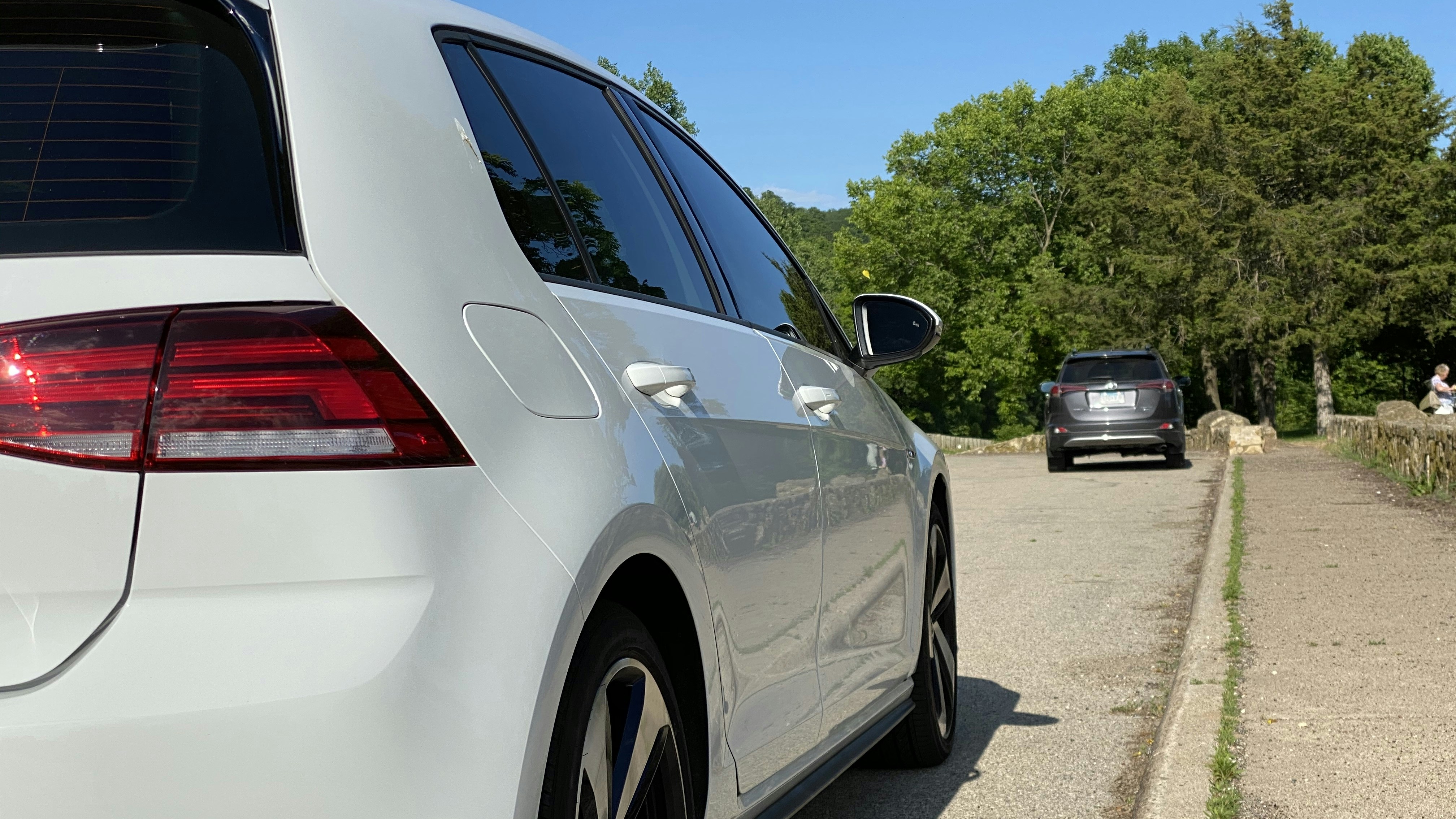 White hatchback parked beside a winding road flanked by lush greenery, with another vehicle in the distance. The scene captures a moment of urban exploration.