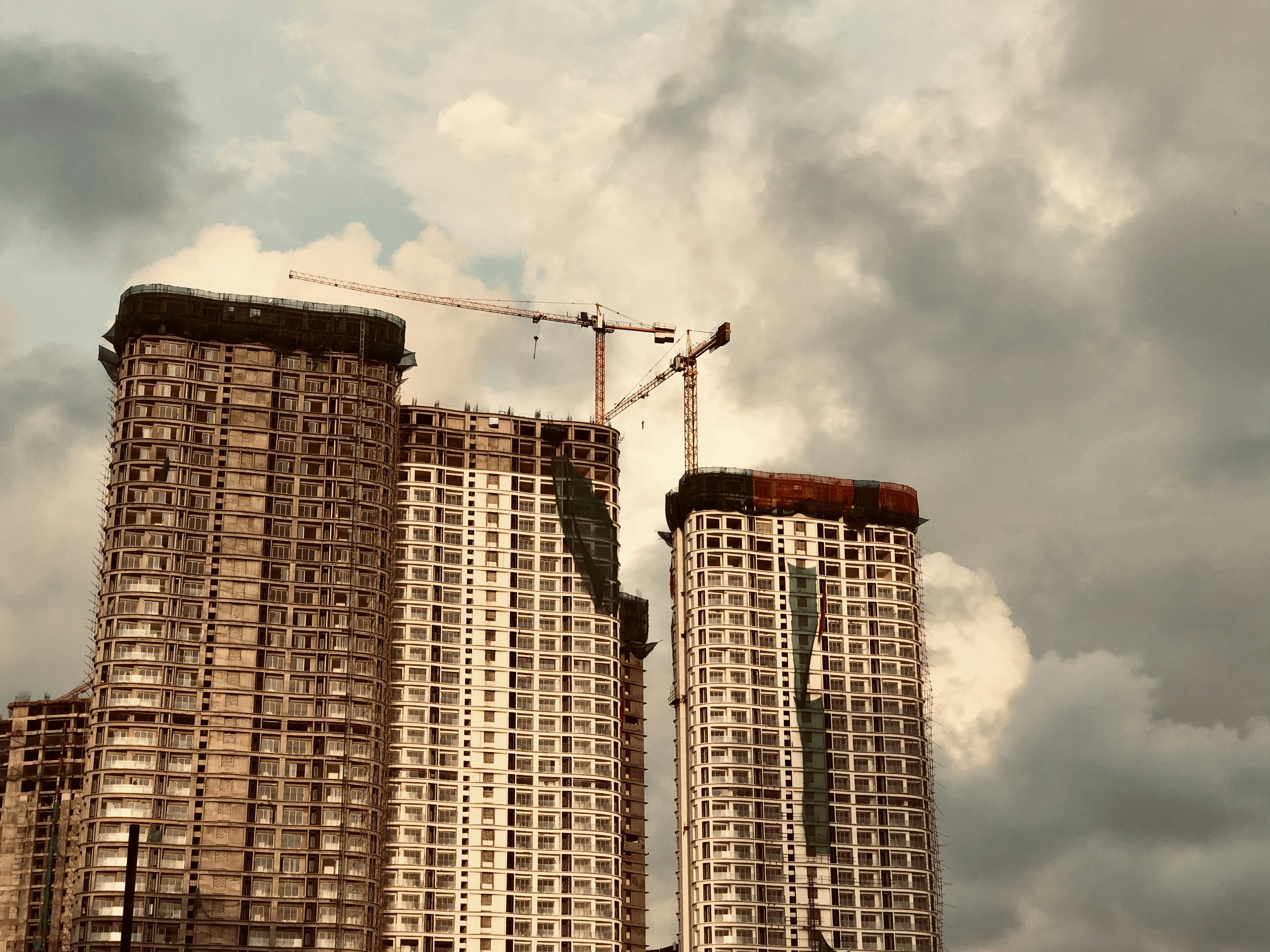 Tall skyscrapers under dramatic cloud cover with a construction crane visible.