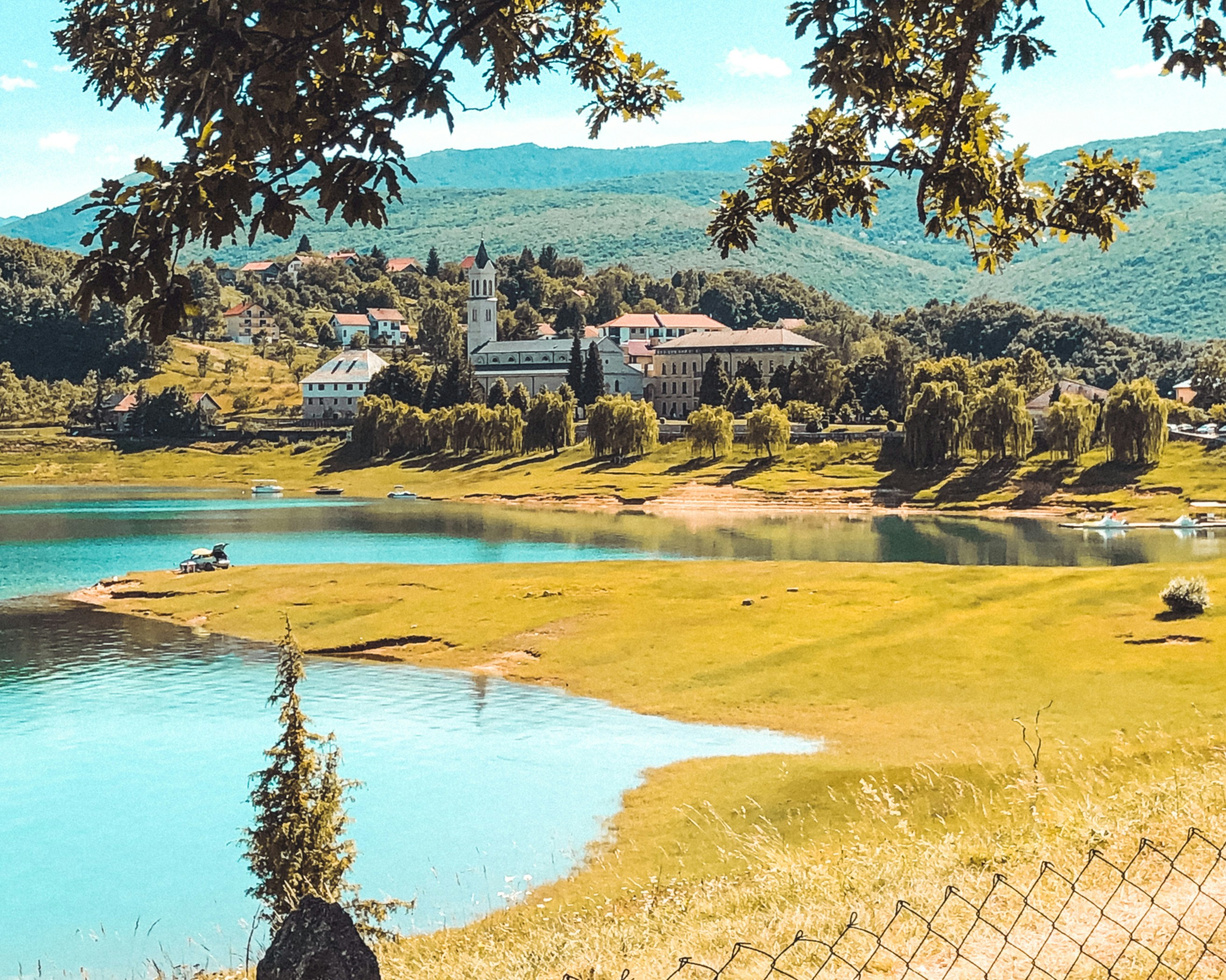 Hilltop Monastery by a Turquoise Lake, Framed by Branches
