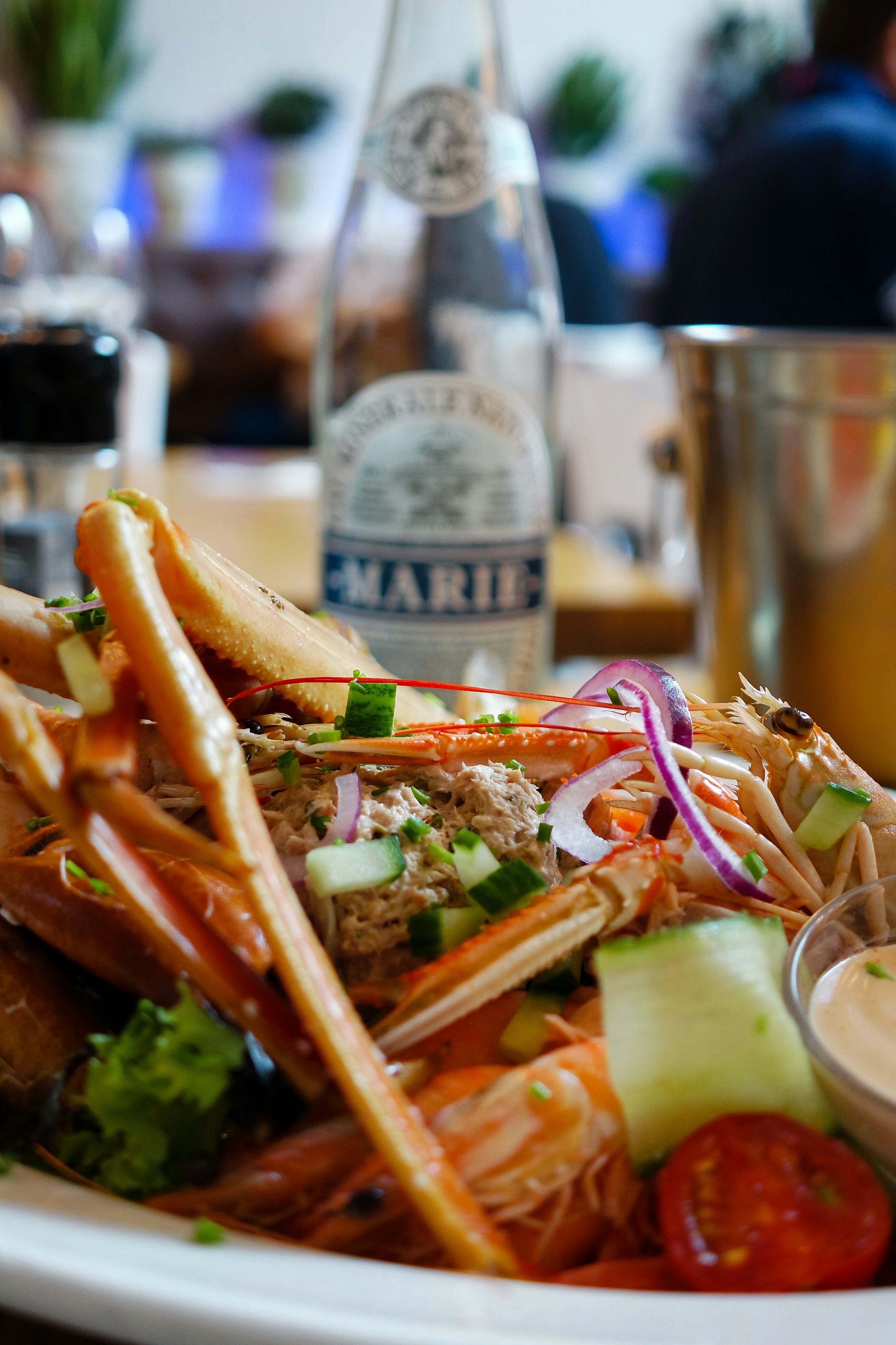 A vibrant seafood dish featuring crab legs, shrimp, and fresh vegetables, accompanied by a bottle of sparkling water. The arrangement showcases a colorful and appetizing feast.