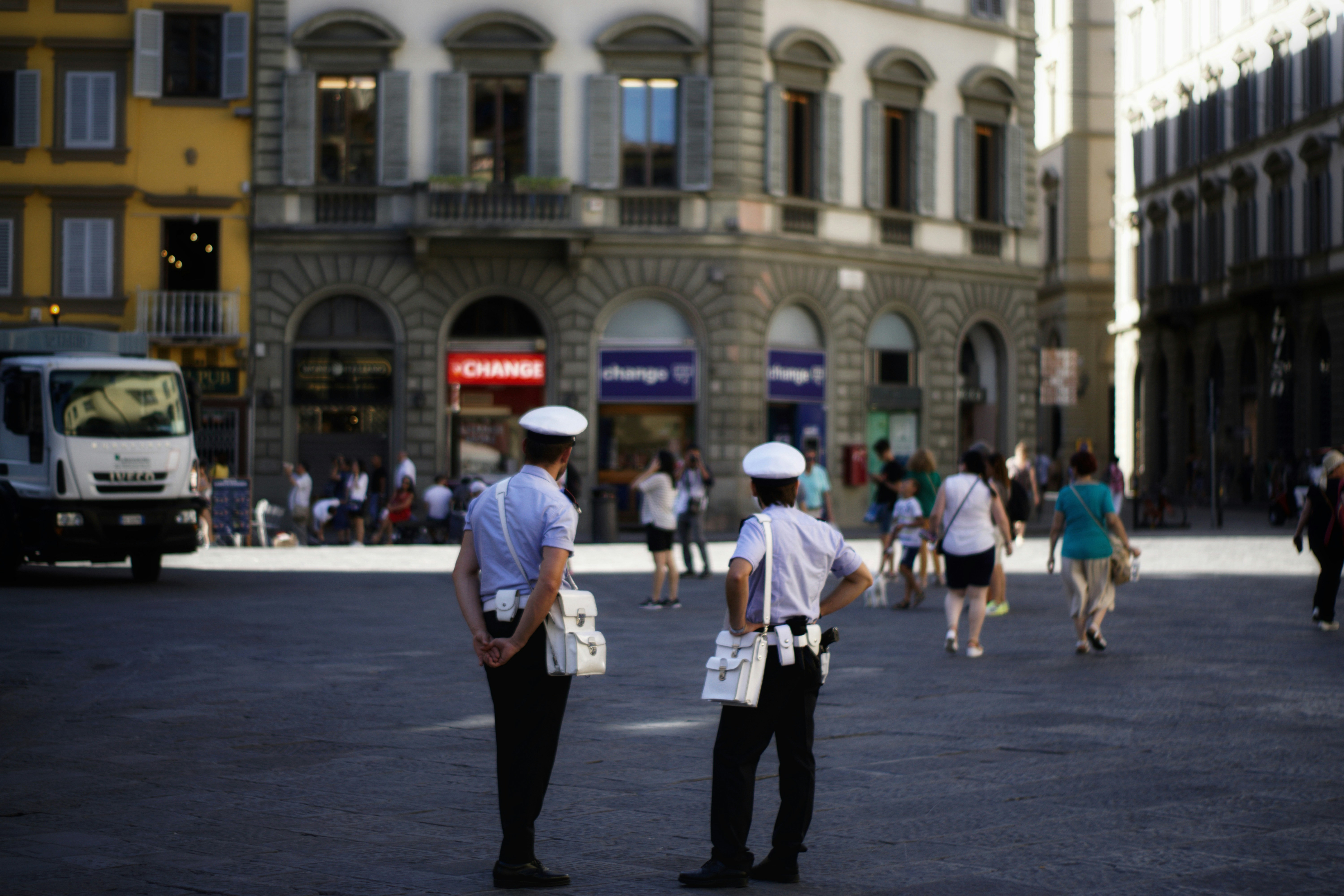 Back to the Crowd: White-Helmeted Officers Hold a Quiet Post in a Sunlit Piazza