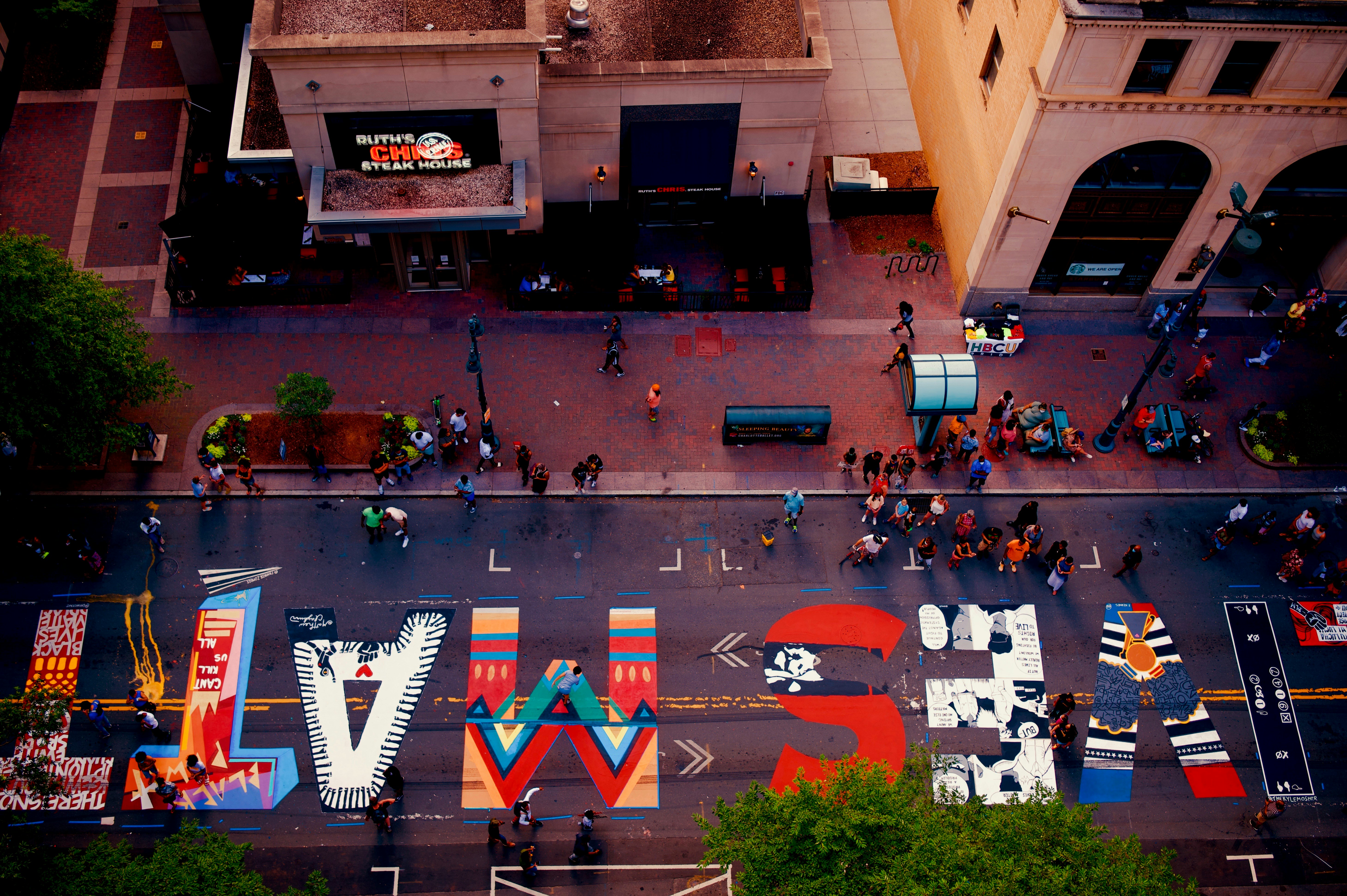 Aerial view of a colorful street mural with people walking along the urban sidewalk.
