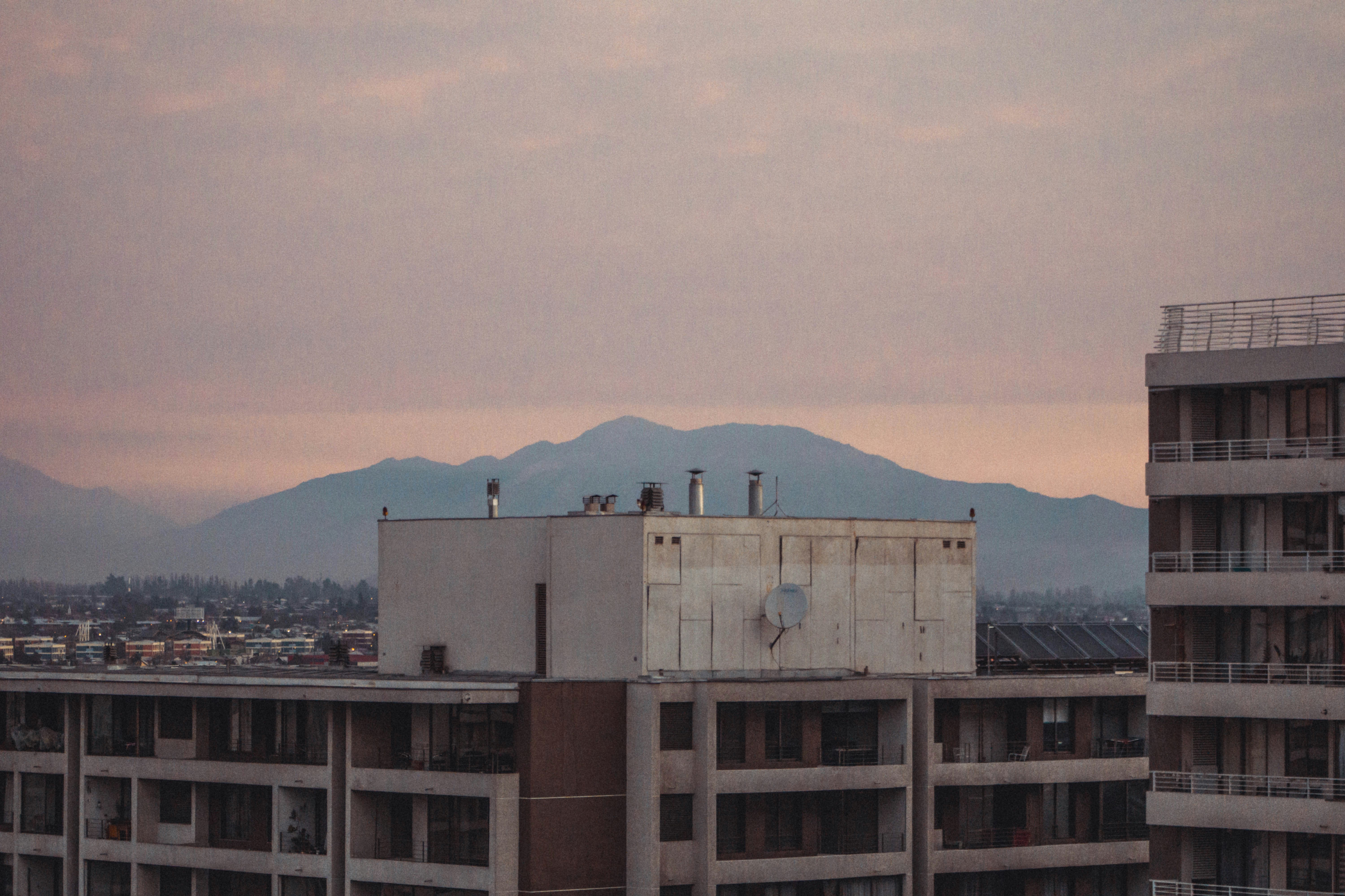 Distant mountains framed by city buildings under a pink evening sky.