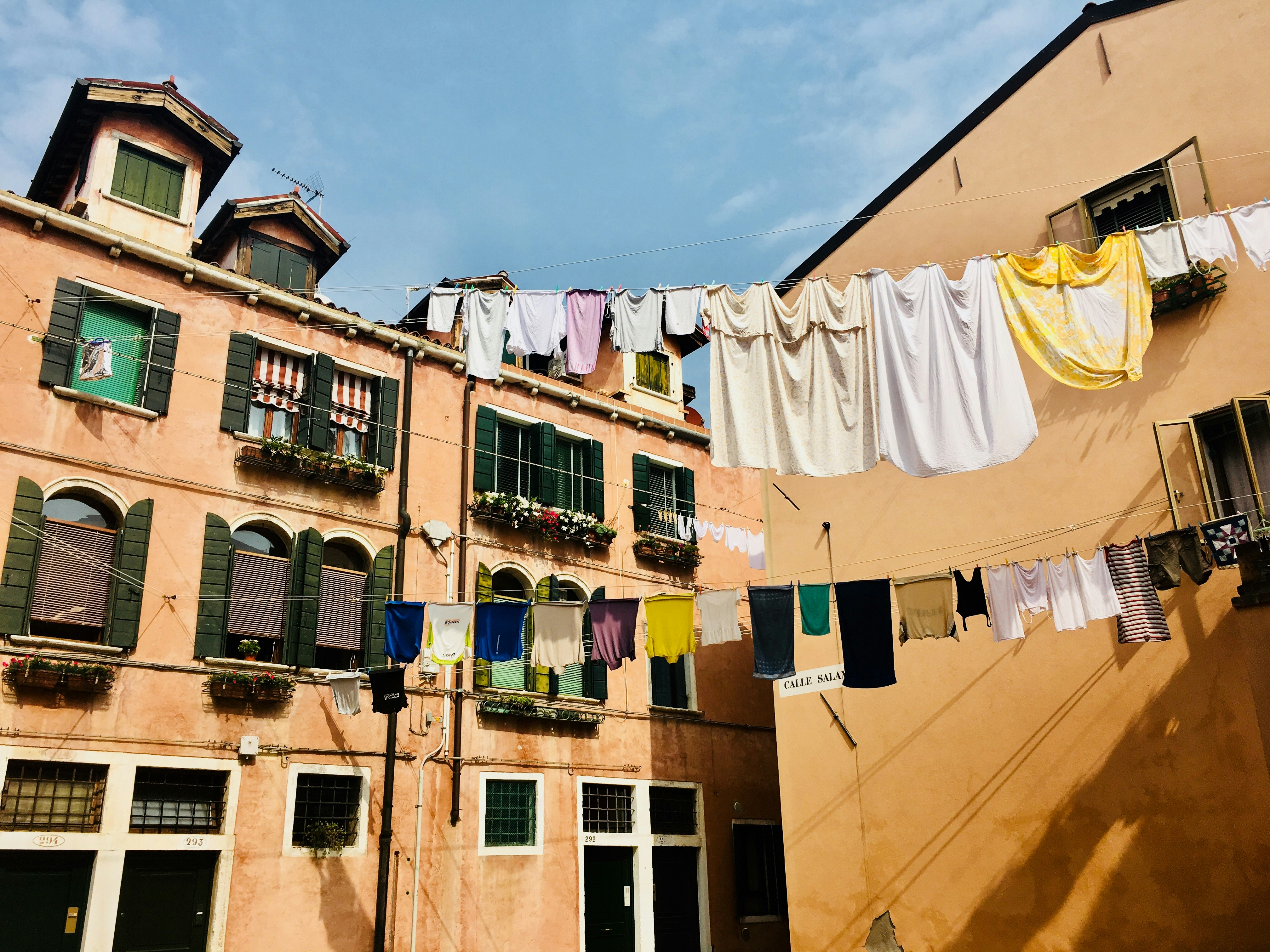 Colorful clotheslines stretch between historic Venetian buildings under a clear blue sky.