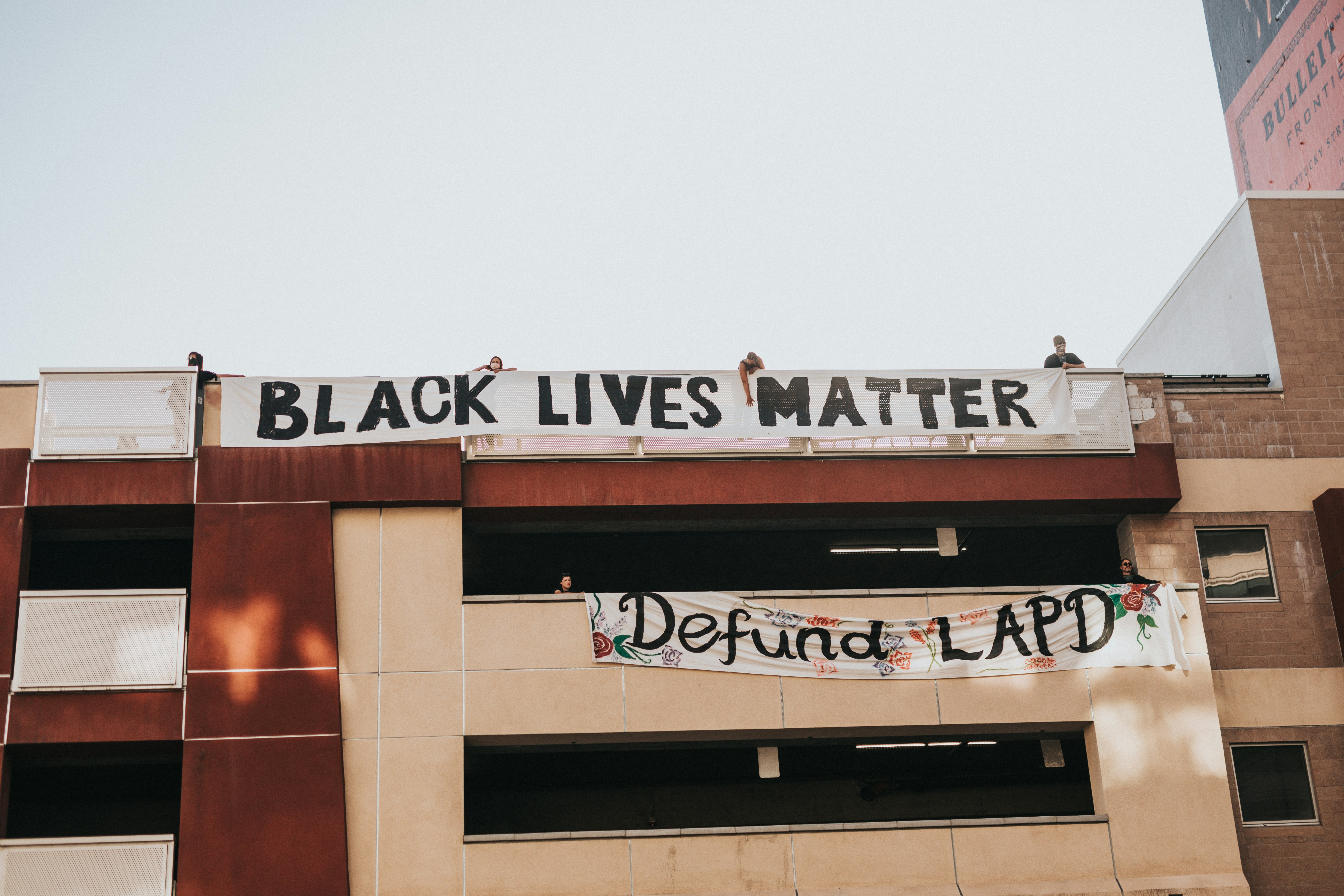 Large banners displaying 'BLACK LIVES MATTER' and 'Defund LAPD' hang from a building, emphasizing a powerful message of social activism.