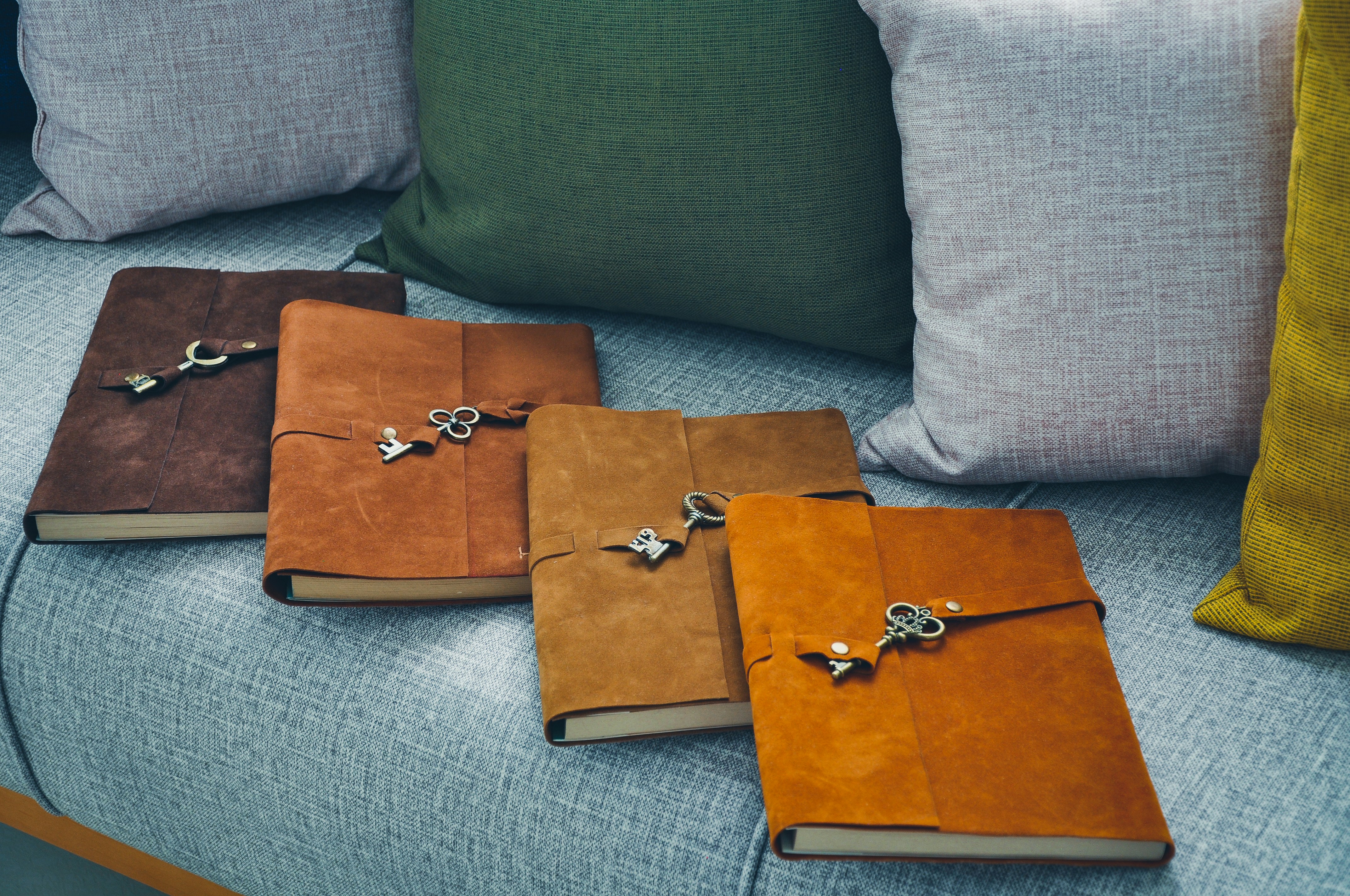 Four leather journals with ornate keys resting on a fabric sofa accented by colorful pillows.