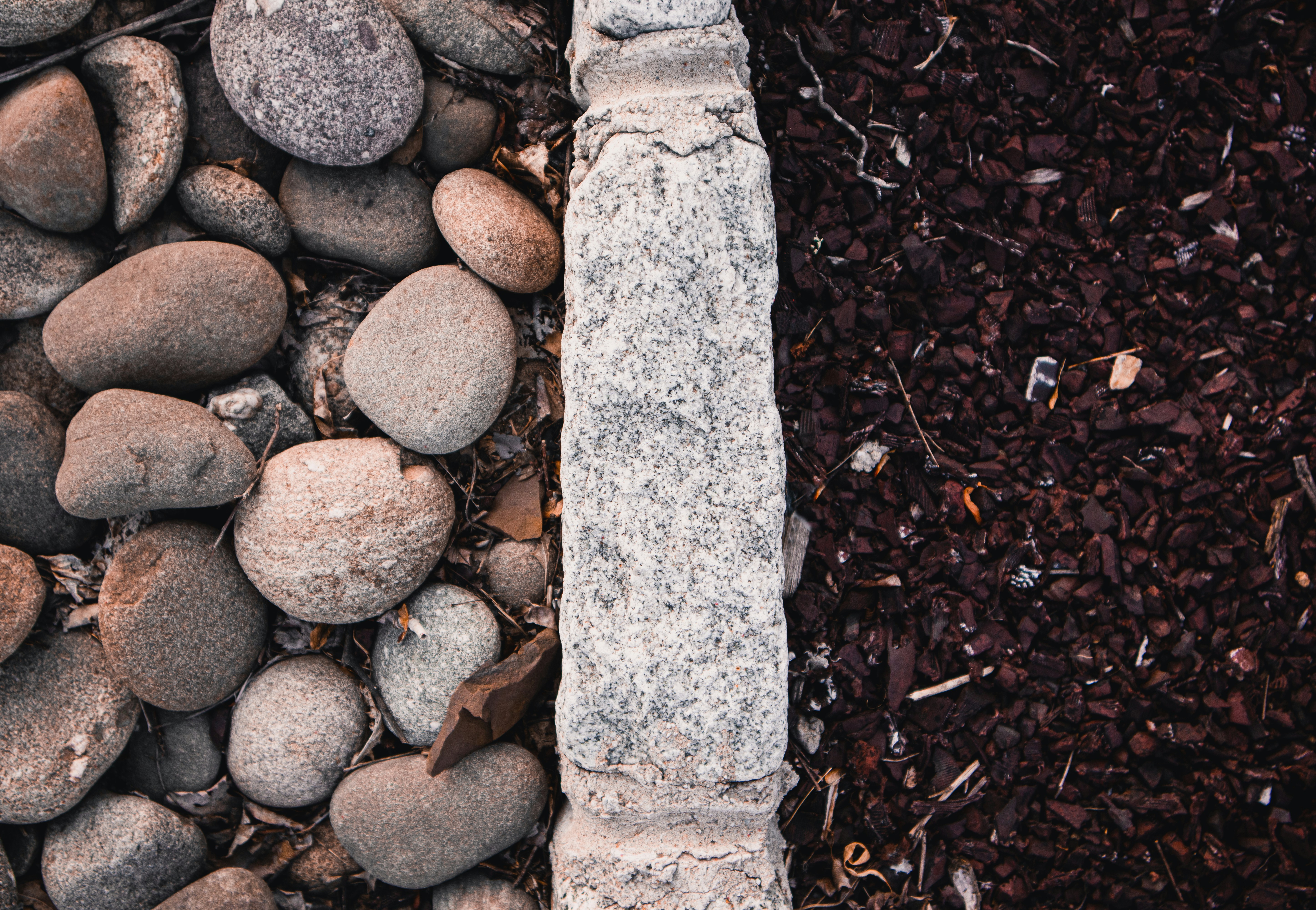 A split view showcasing smooth pebbles on one side and dark mulch on the other, separated by a textured stone border.
