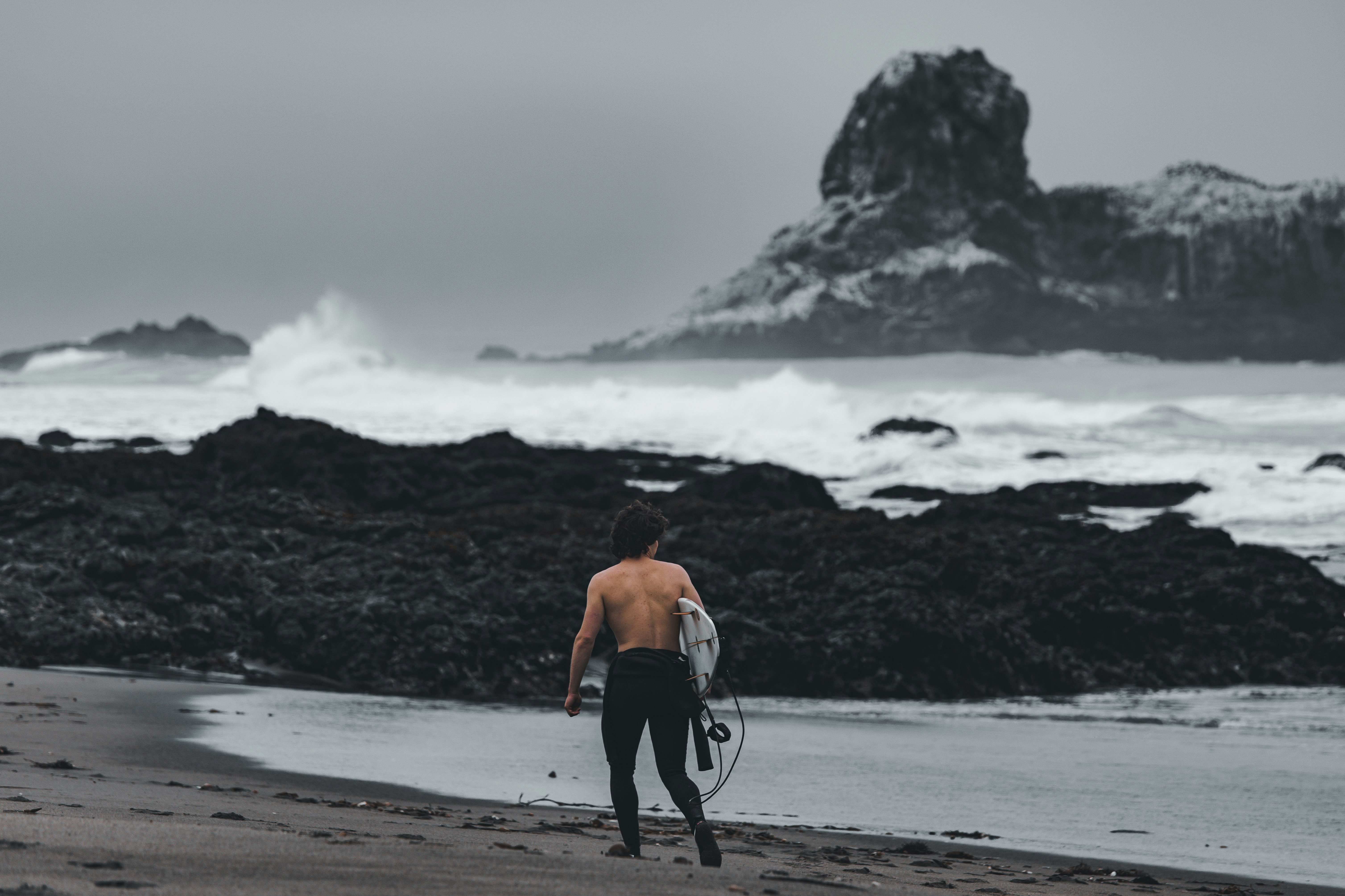 Topless man in black pants and black shoes walking on beach shore ...