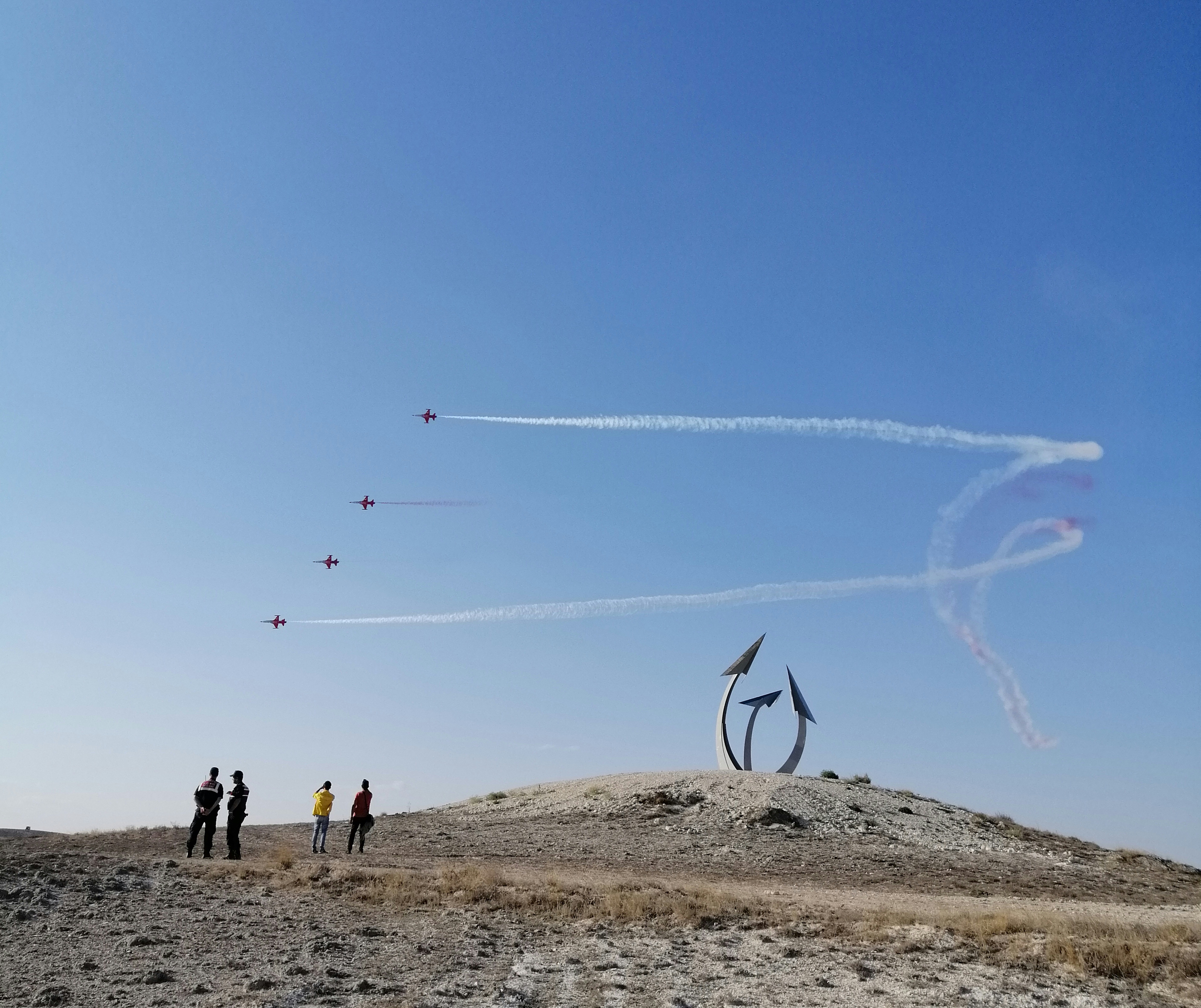 F5 jets perform an aerial display over a hilltop monument with spectators watching from below.