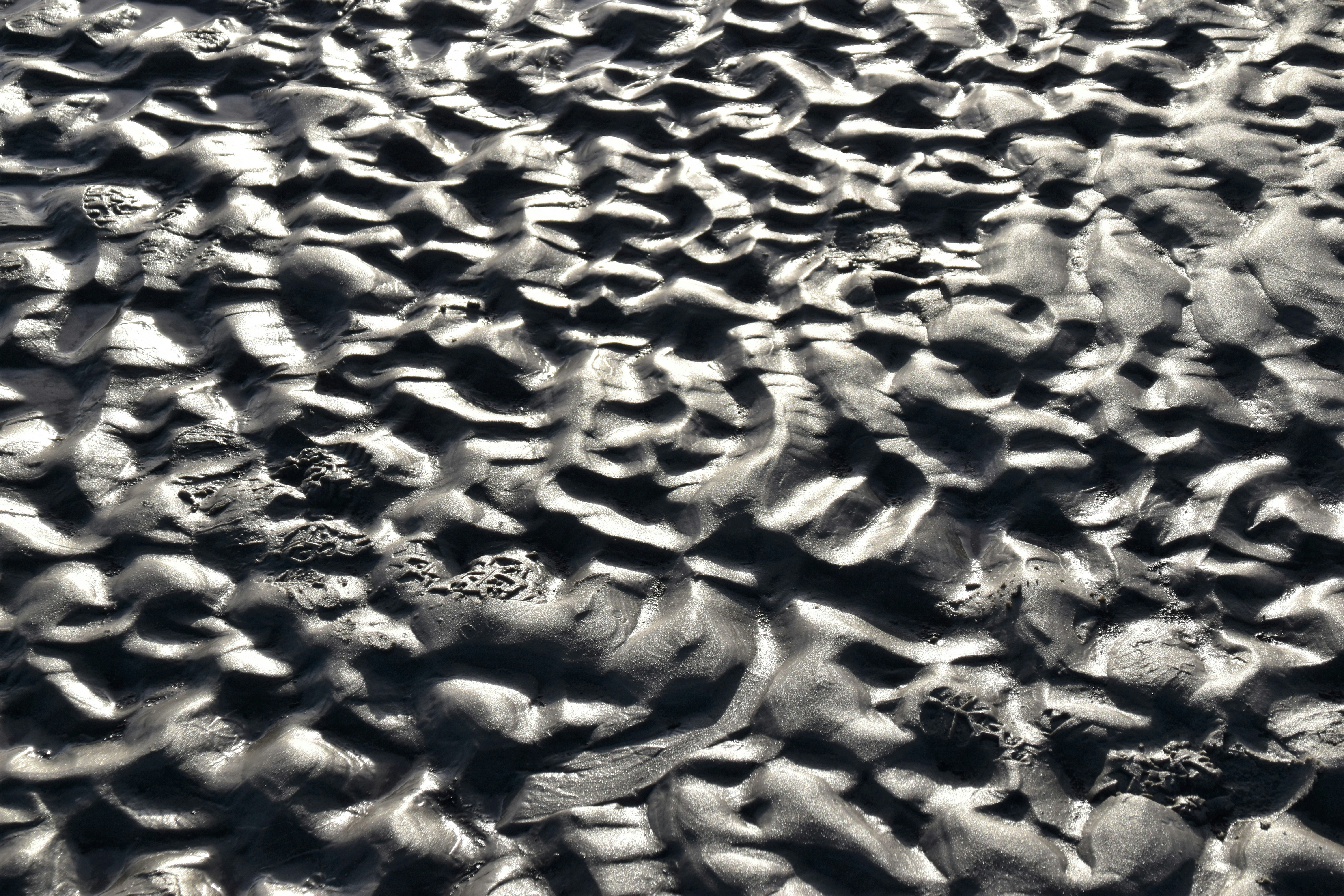 Intricate patterns of wet sand captured in soft light, revealing the dynamic interplay of nature's elements.