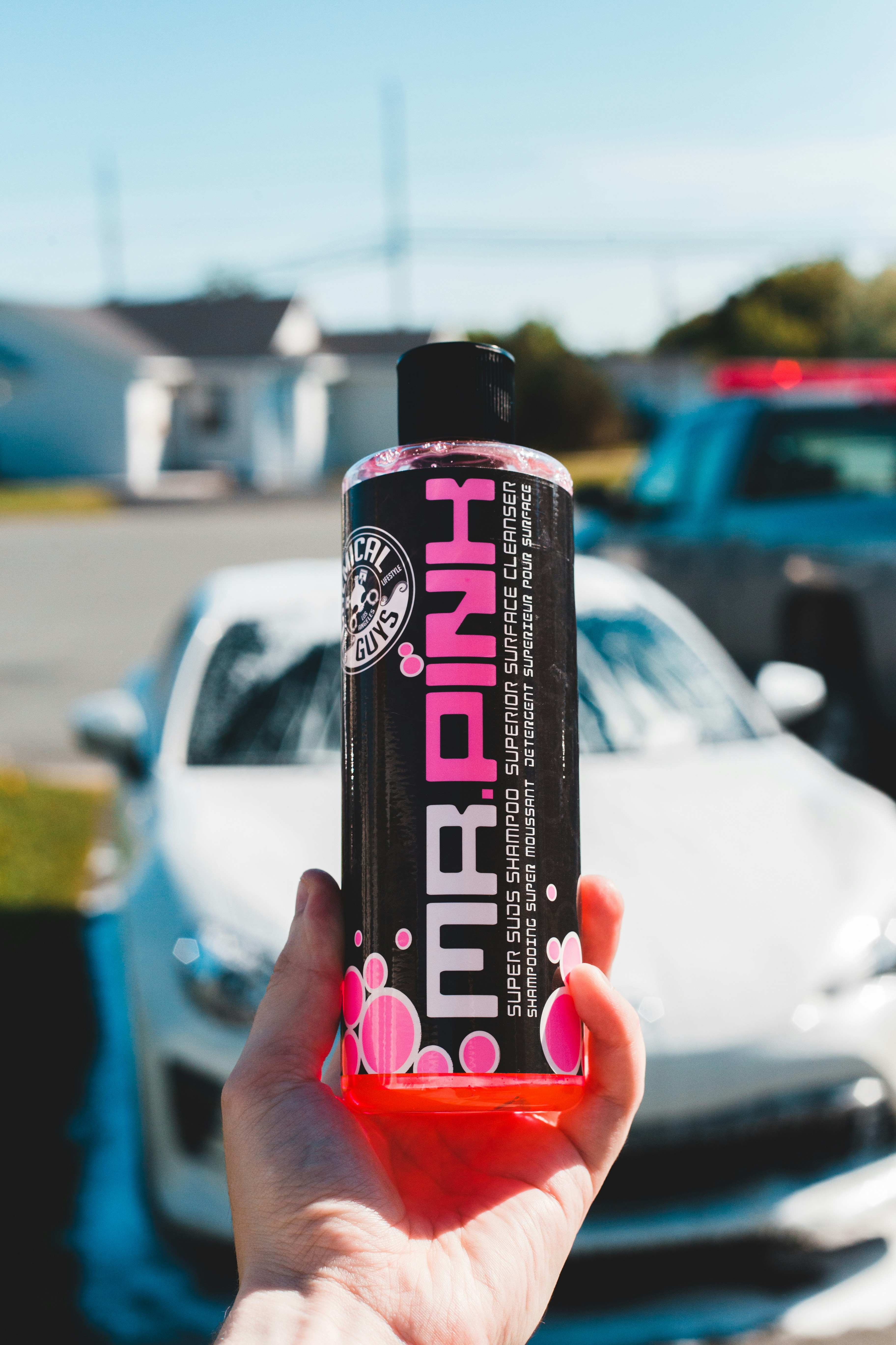 Mr. Pink Shine: Handheld Car-Wash Elixir Framing a Sunlit Vehicle