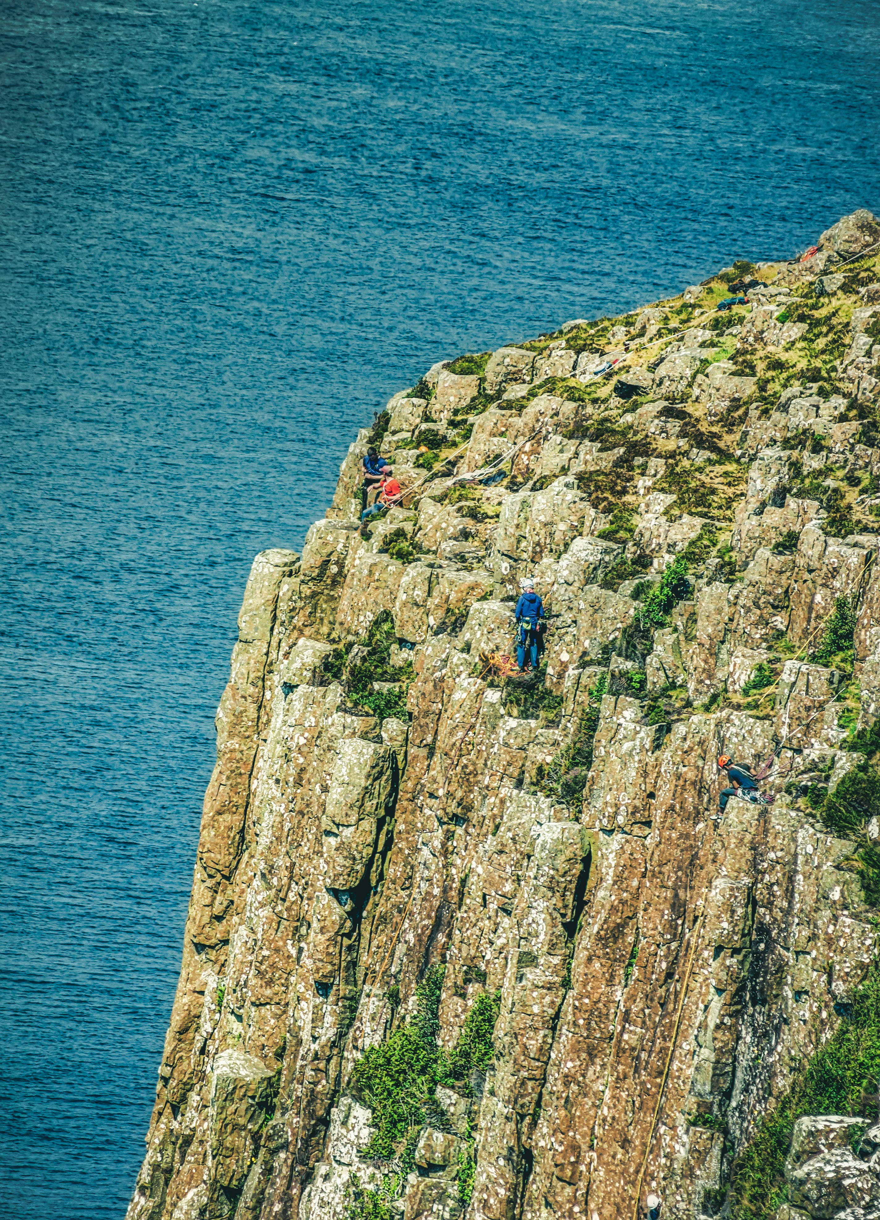 Climbers navigate a rugged cliff face overlooking the ocean, showcasing the thrill of rock climbing against a stunning natural backdrop.