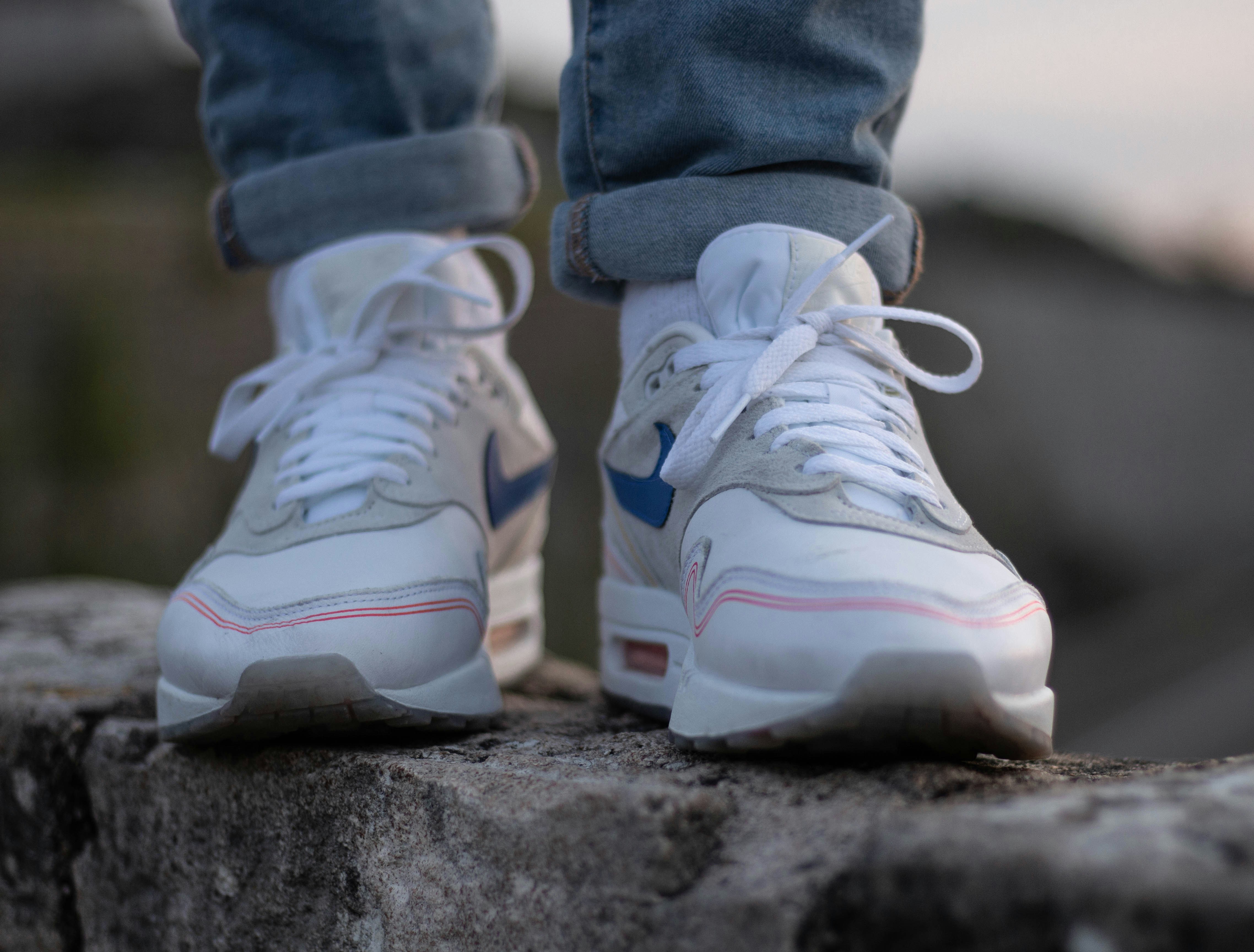 White and purple Nike sneakers paired with blue denim jeans standing on a stone ledge.
