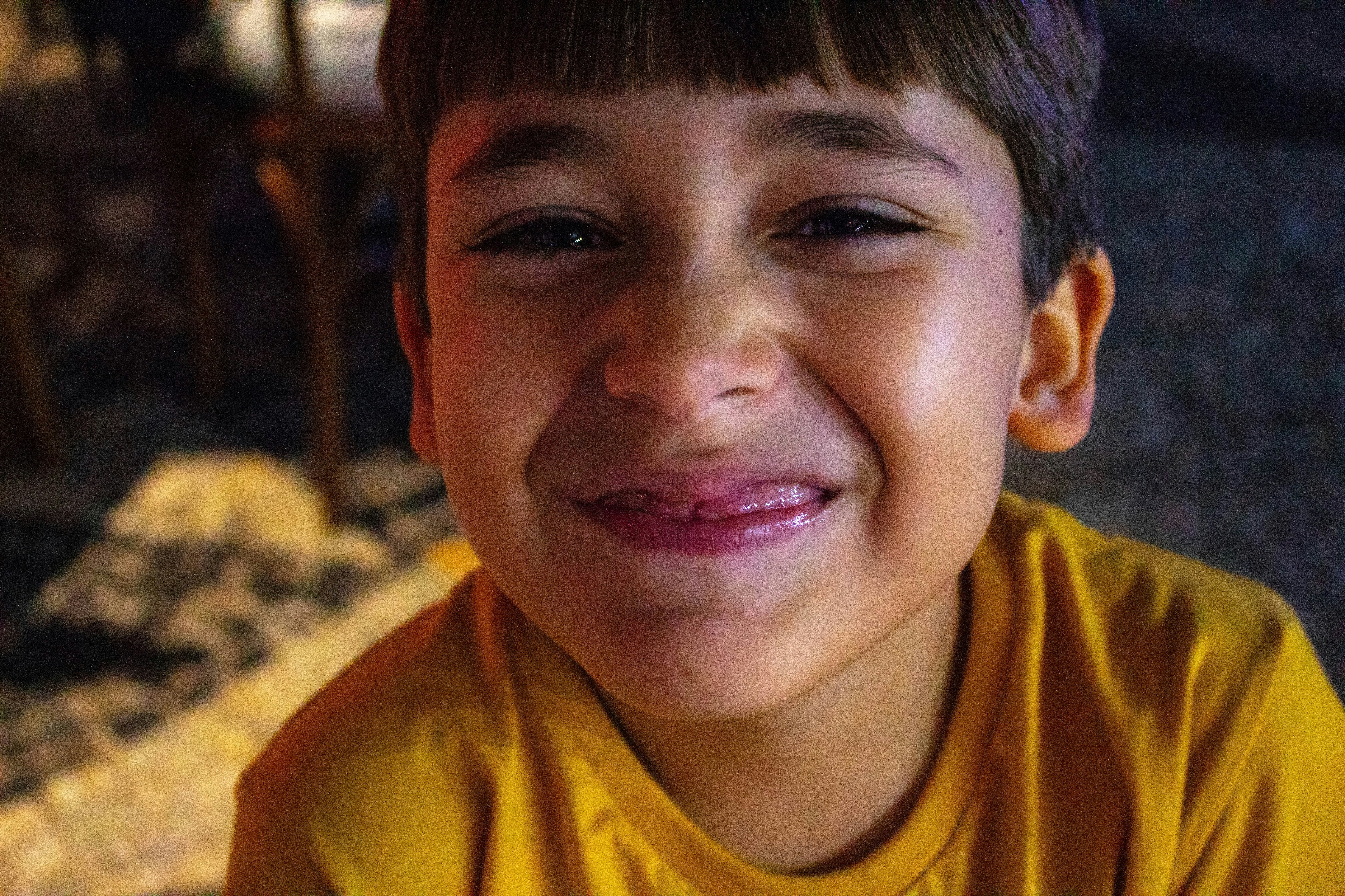 Young boy in a yellow shirt smiling warmly in soft, dim lighting.